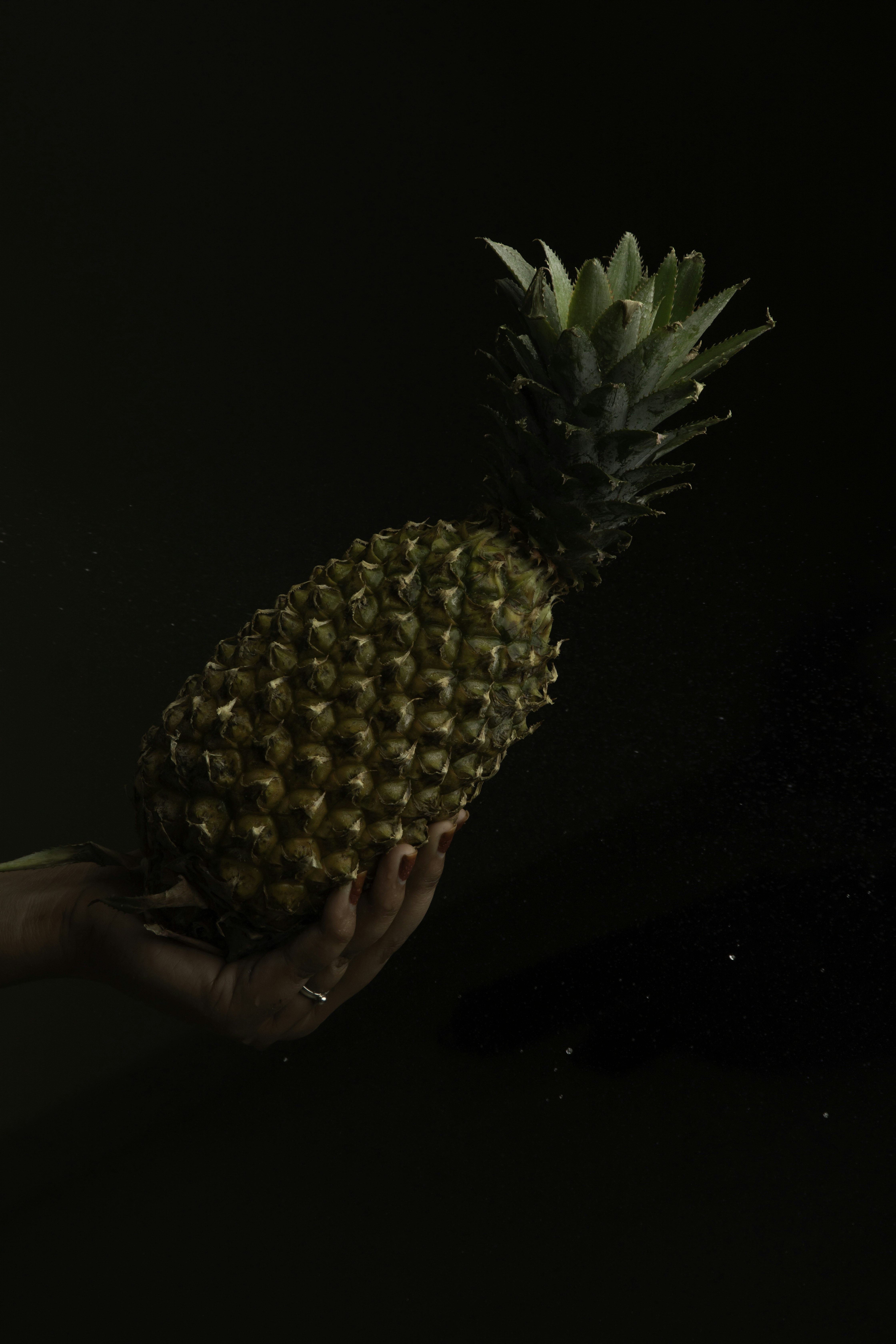 A hand presenting a ripe pineapple against a dark backdrop, highlighting its textured surface and vibrant crown. 