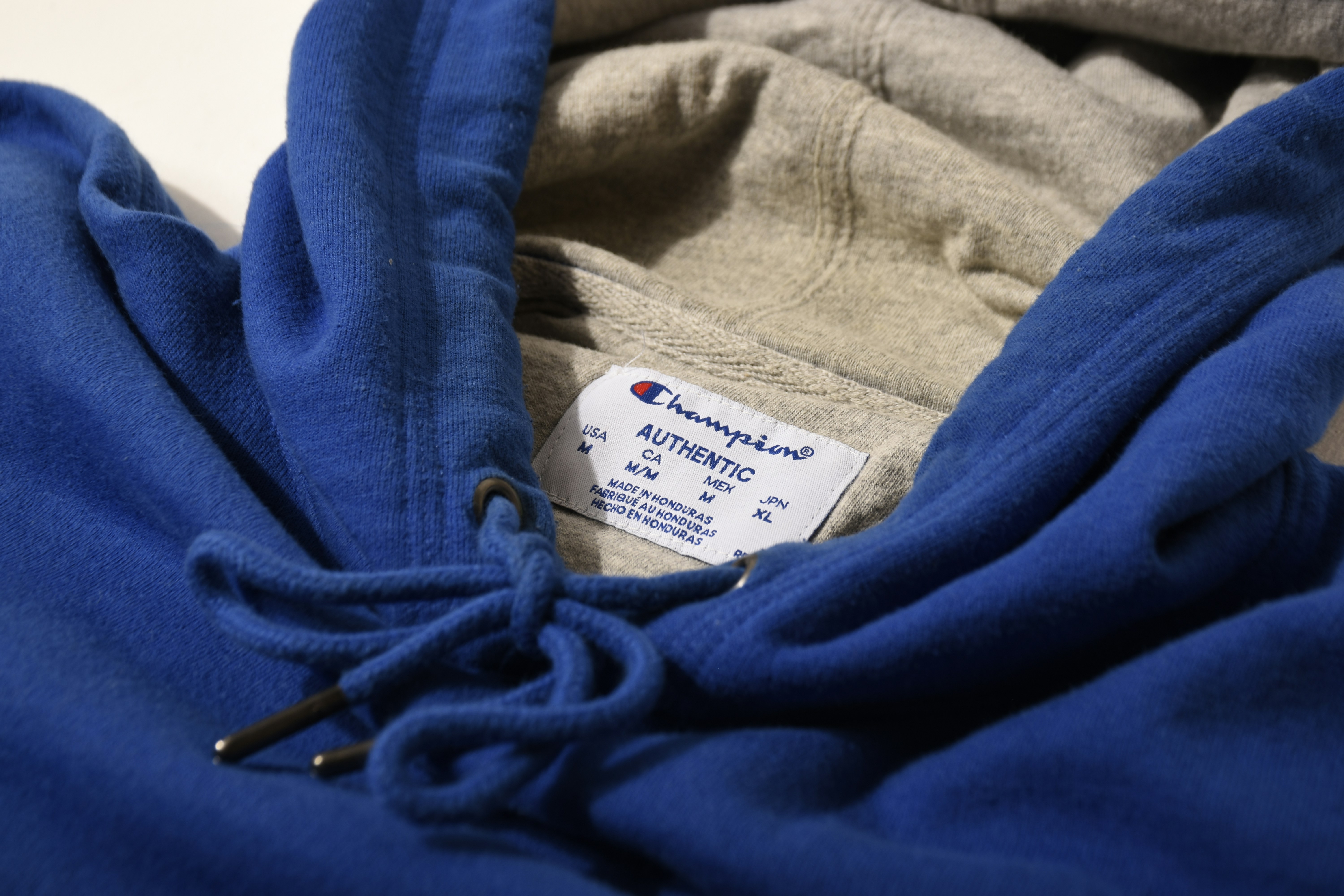 Close-up of a blue Champion hoodie showcasing its inner lining and care label. The focus highlights the quality and detail of the fabric.