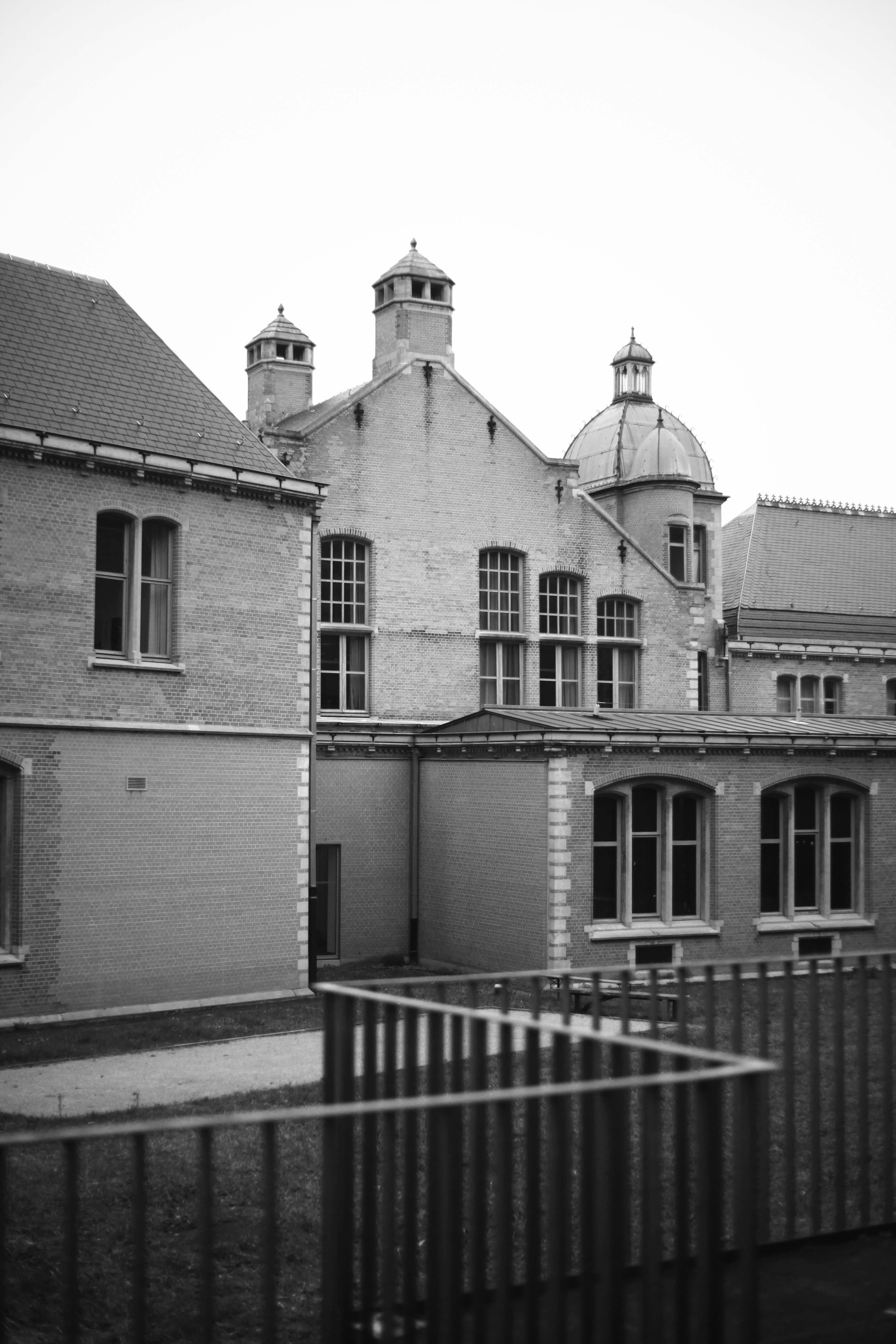 A historic building featuring intricate architectural details, captured in monochrome. The structure showcases a blend of styles with prominent domes and large windows.