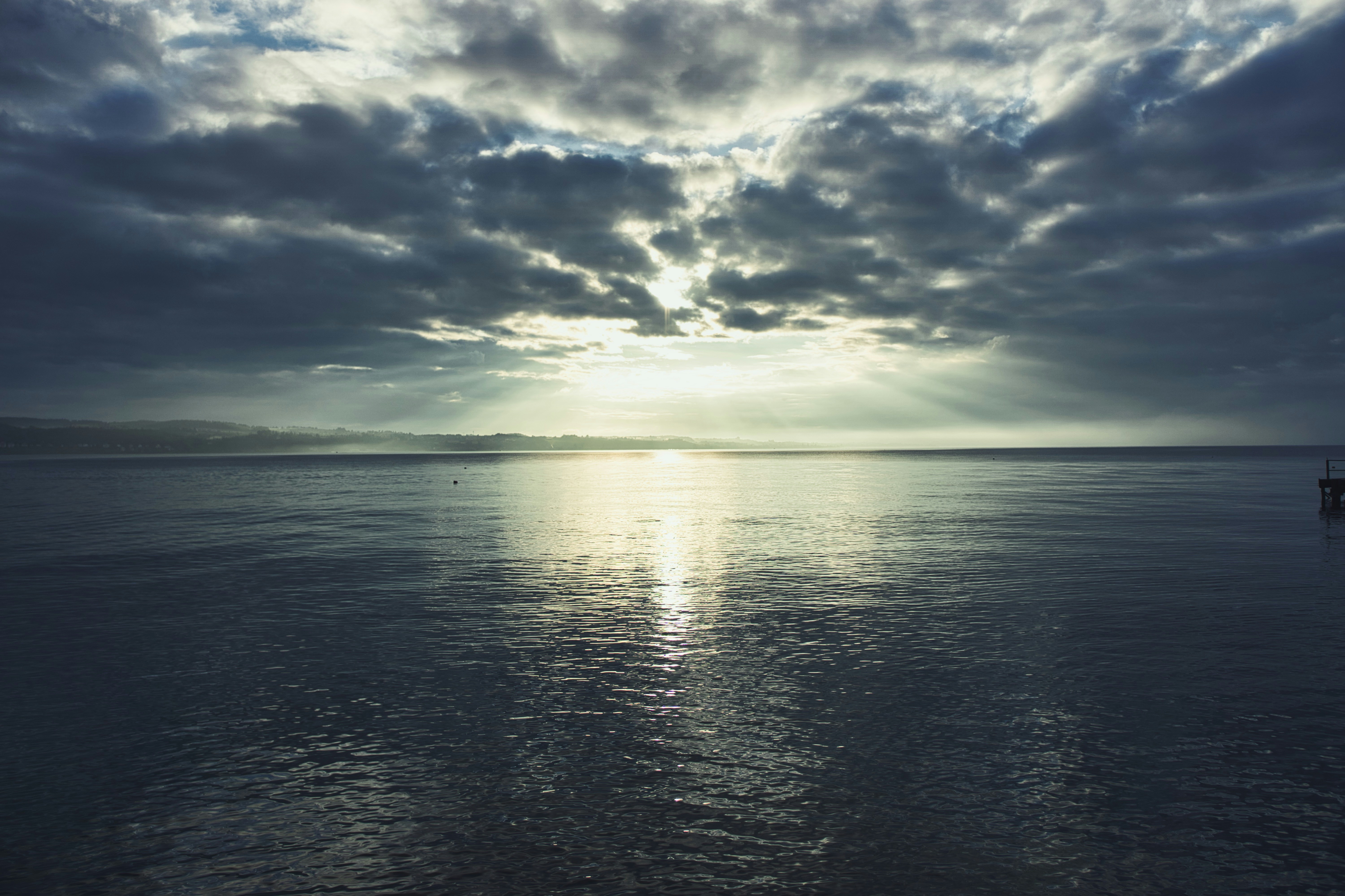 Sunlight breaking through dramatic clouds, reflecting on a calm ocean at dawn.