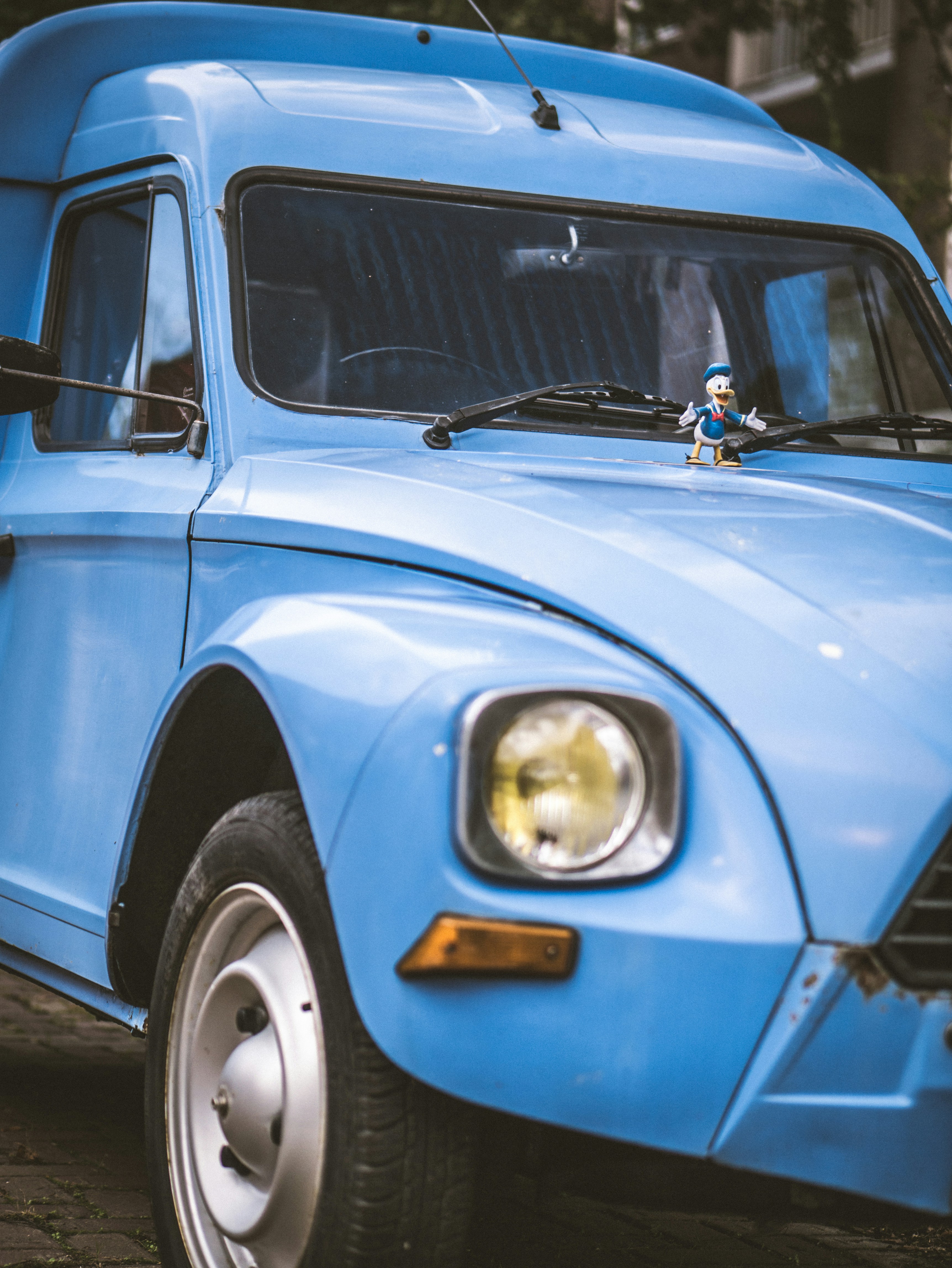 A vintage blue vehicle with a playful Donald Duck figurine perched on the dashboard, showcasing a charming blend of nostalgia and character.