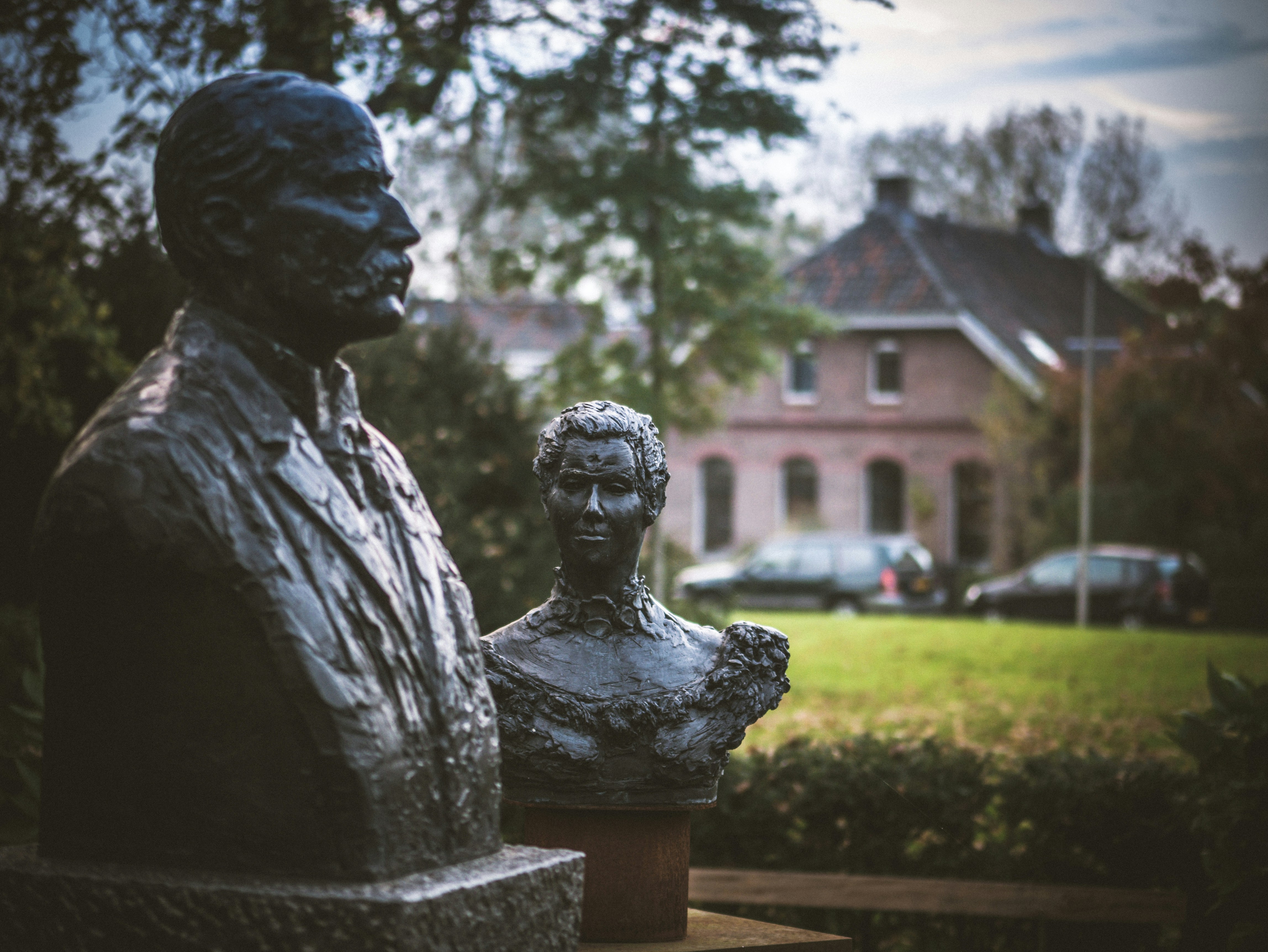 Bronze busts of two historical figures set against a serene park backdrop, capturing a moment of reflection in a tranquil environment.