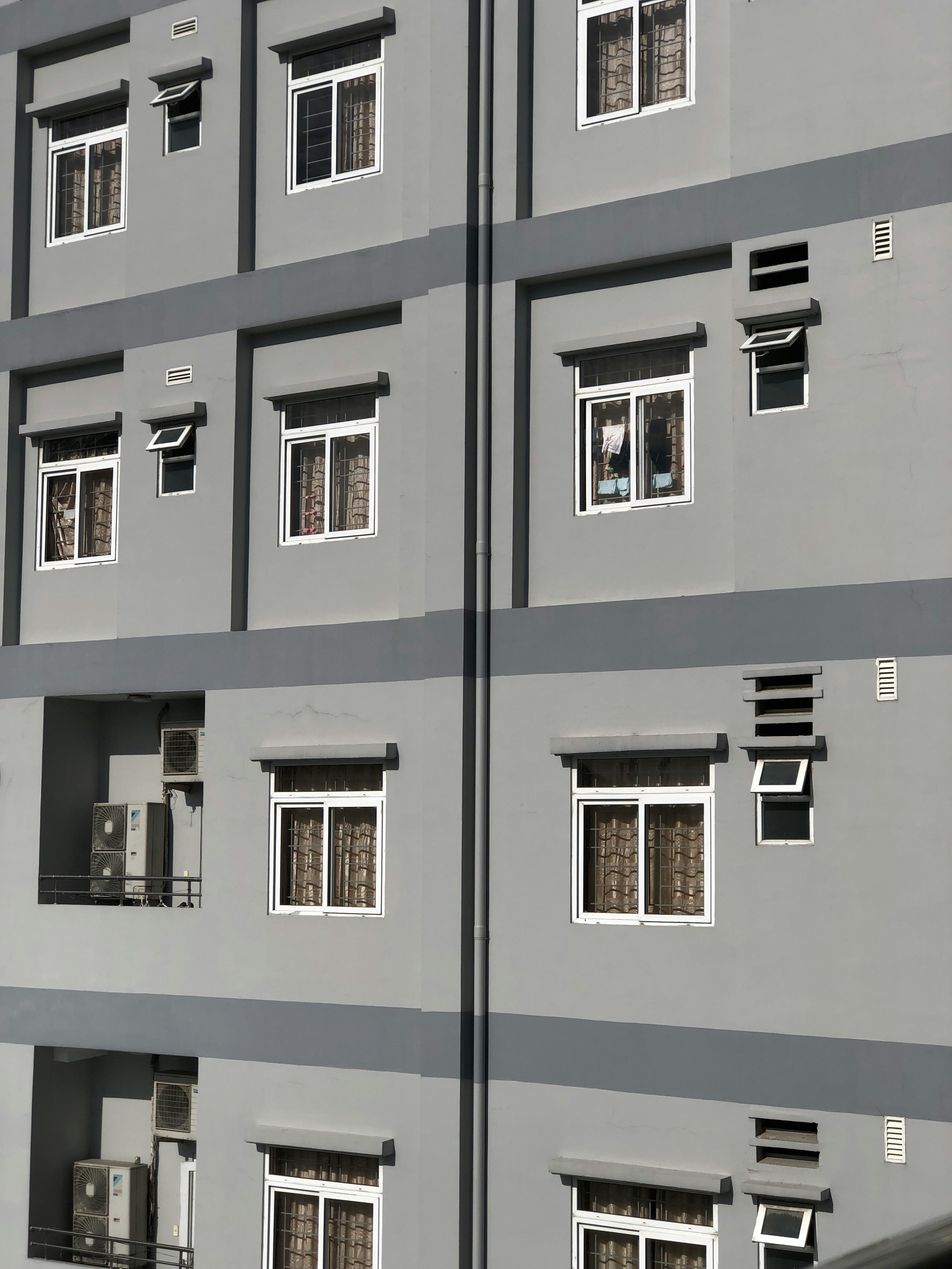 A close-up view of a modern building's facade featuring a series of windows and air conditioning units, showcasing urban architecture.