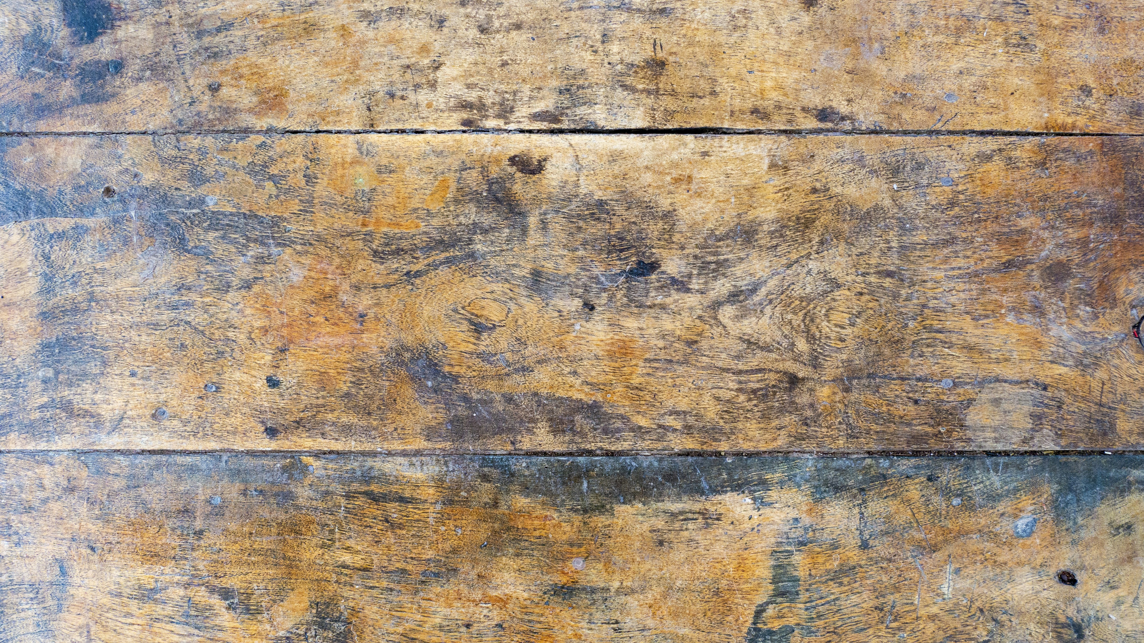 Close-up view of a rustic wooden surface showcasing intricate grain patterns and natural wear. The rich tones and textures highlight the character of the material.
