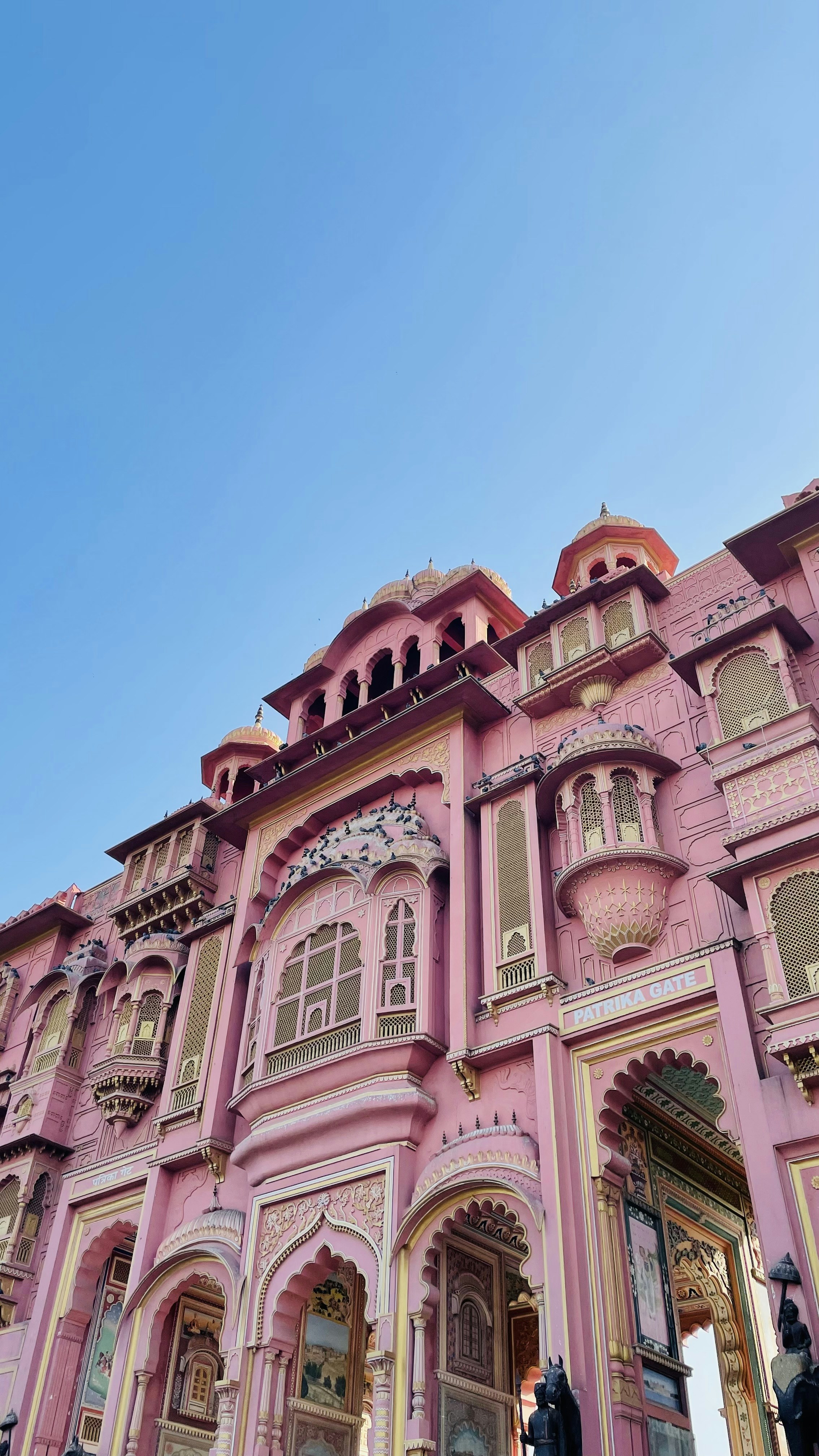 Intricate architectural details of a vibrant pink building in Jaipur, showcasing traditional Indian design elements. The structure features ornate arches and decorative motifs.