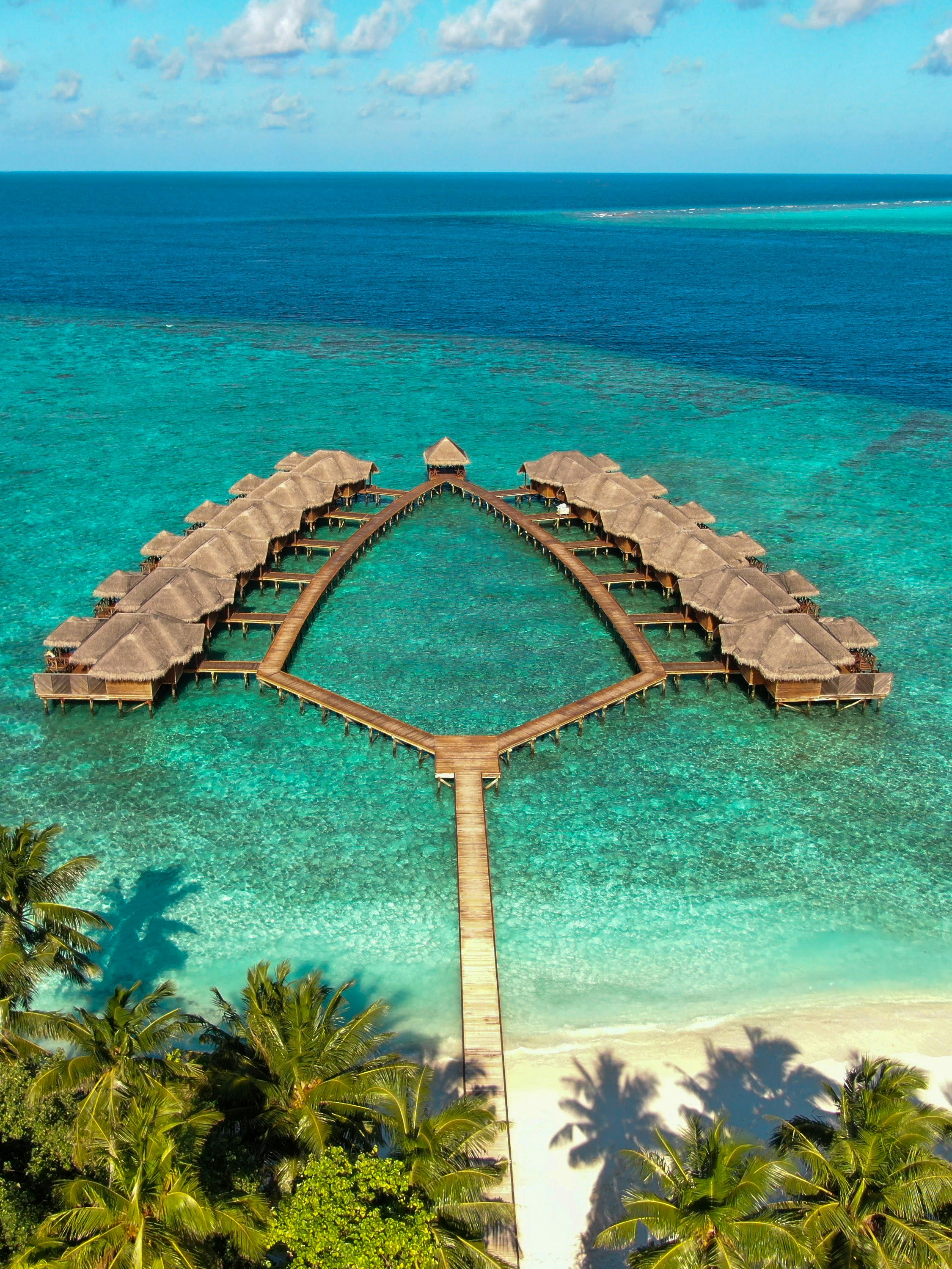 Overwater bungalows arranged in a symmetrical pattern, surrounded by turquoise waters and lush greenery.