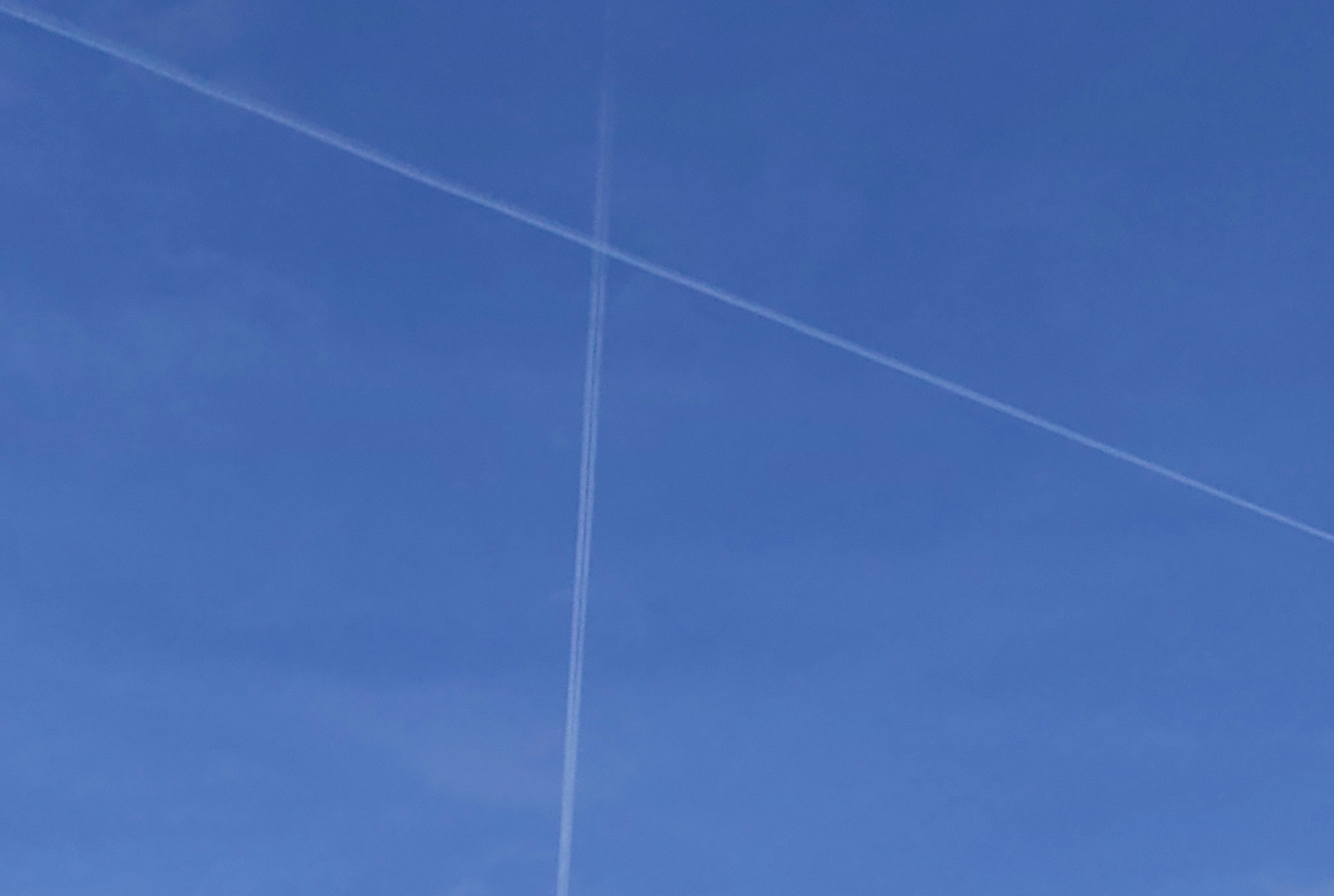 Contrails crisscrossing a clear blue sky, creating a geometric pattern of lines. The scene captures the interplay of aviation and nature.