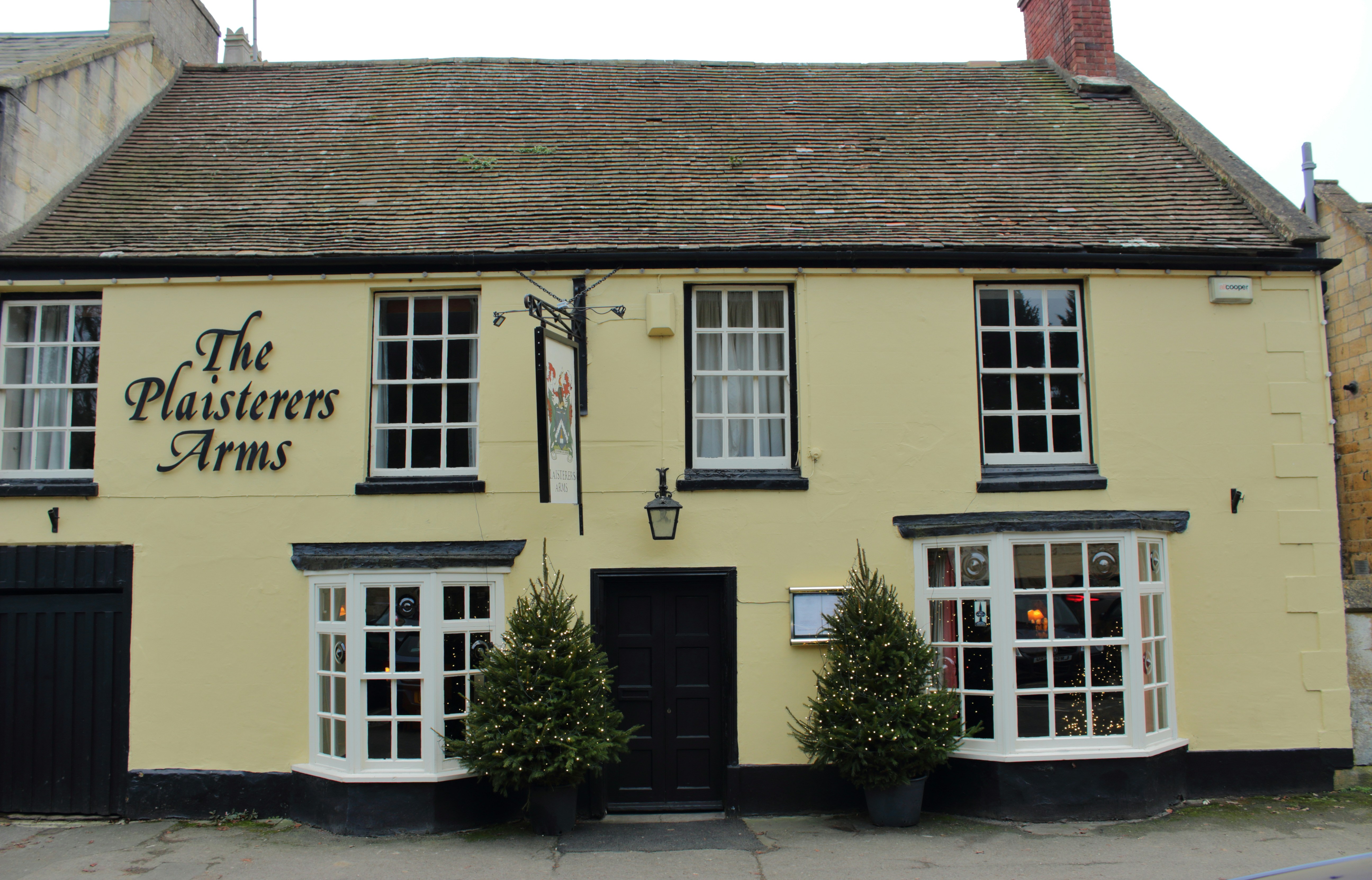 Charming pub facade featuring large windows and decorative greenery, inviting patrons to enjoy a warm atmosphere.