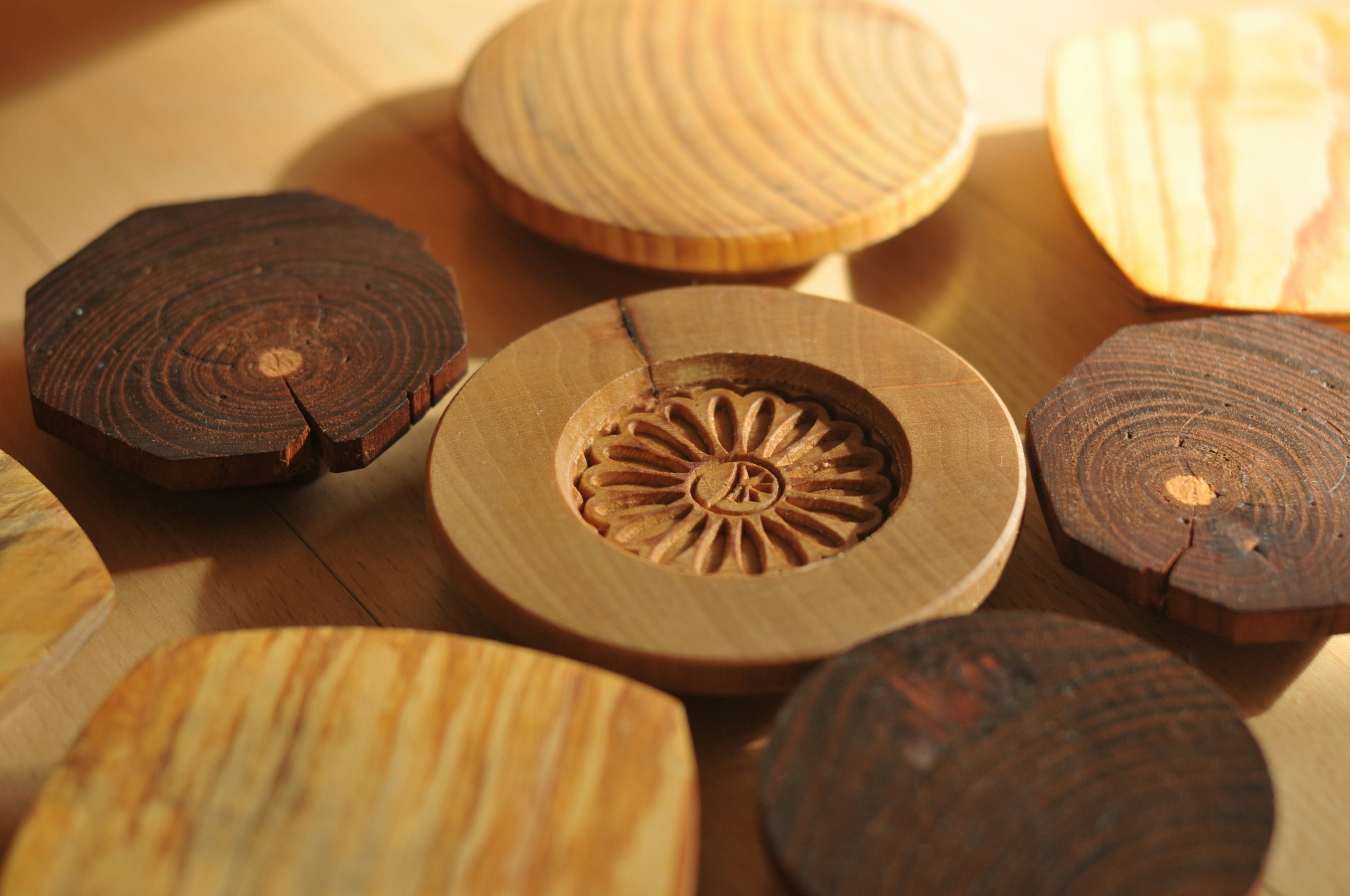 Intricately designed wooden coasters arranged on a surface, showcasing various textures and patterns. The central piece features a floral carving.