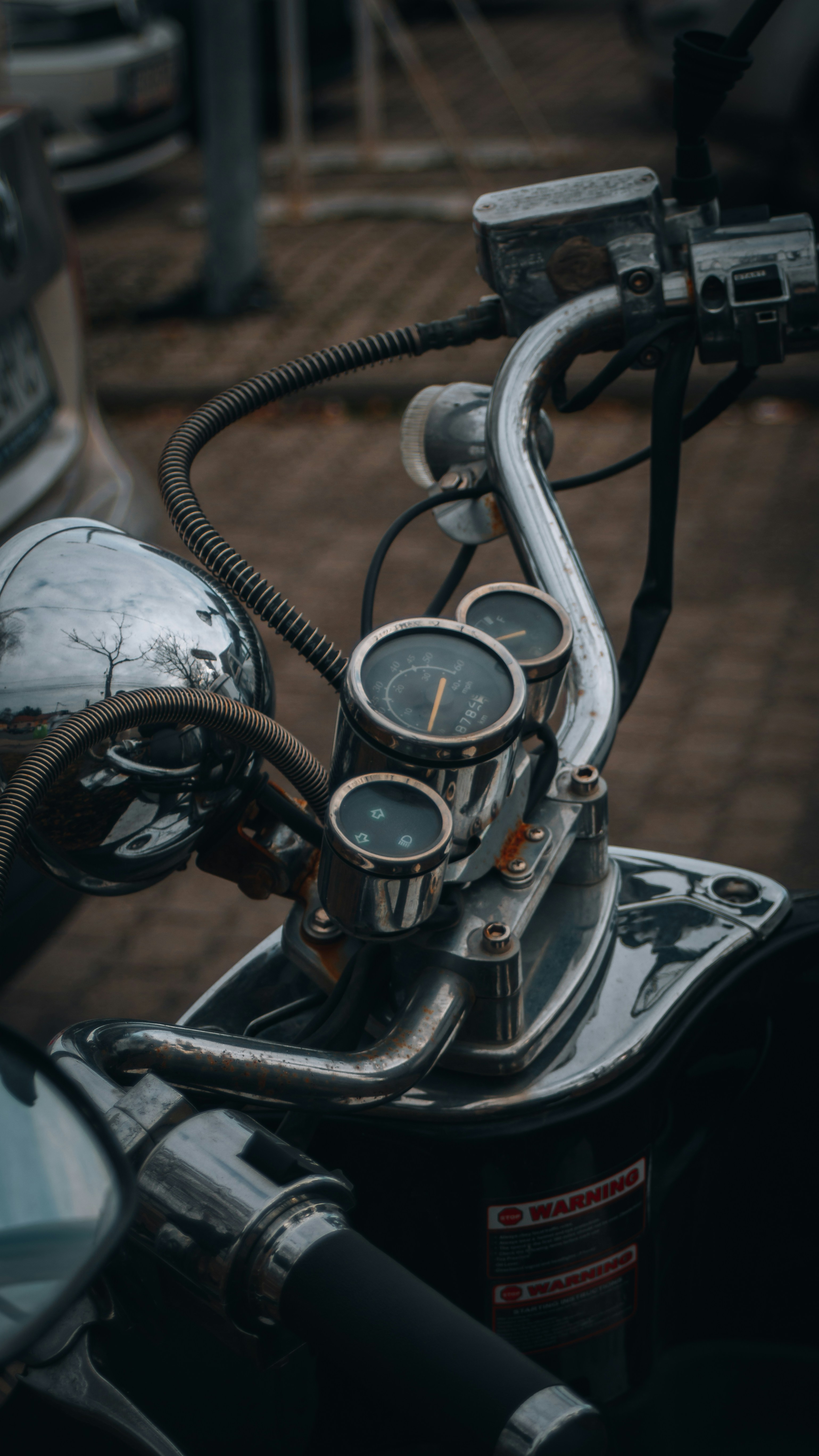 Close-up of a motorcycle's handlebar featuring chrome gauges and intricate detailing. The reflective surfaces add depth to the composition.