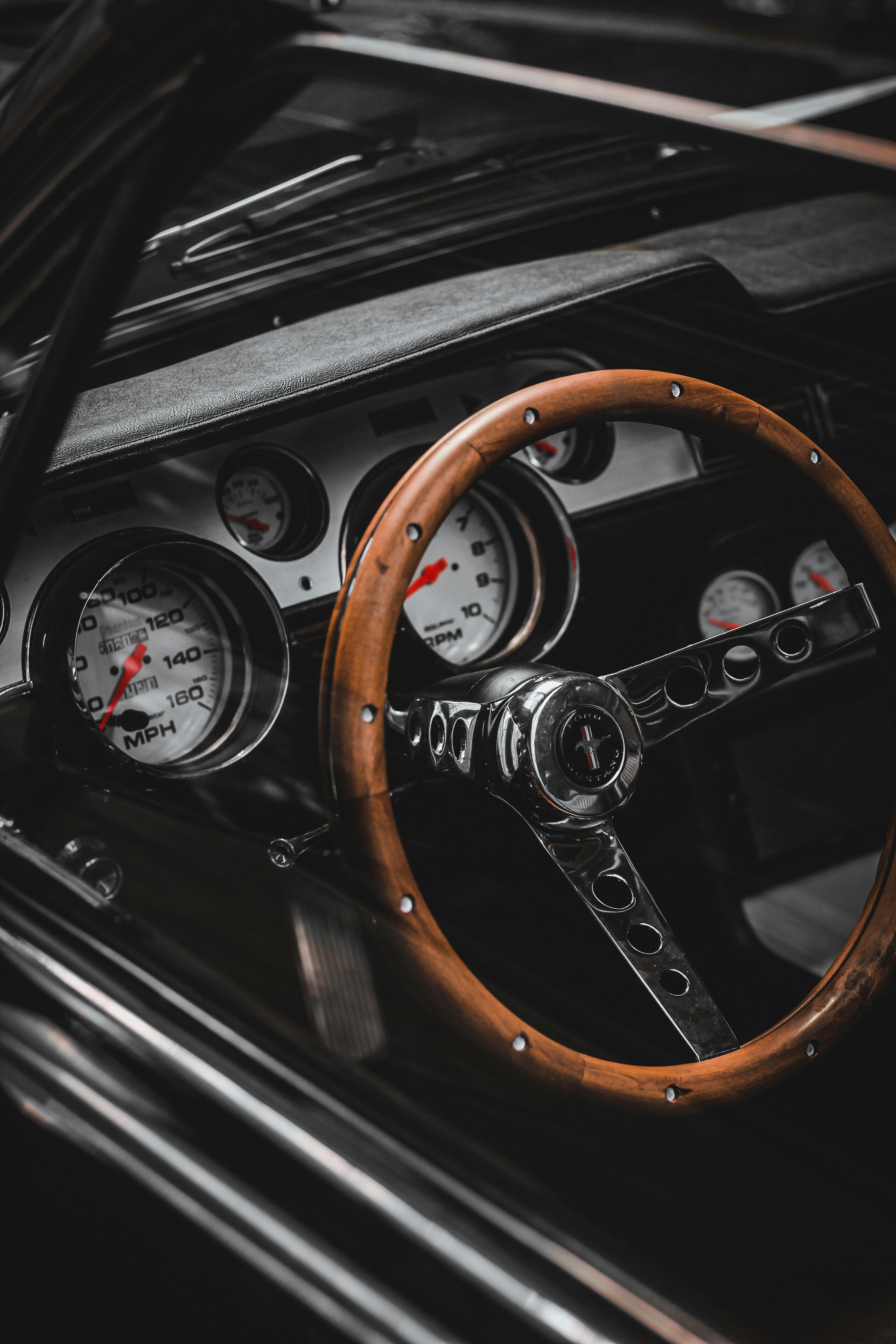 Close-up of a vintage car's dashboard featuring a wooden steering wheel and retro gauges. The intricate details highlight the craftsmanship of classic automotive interiors.
