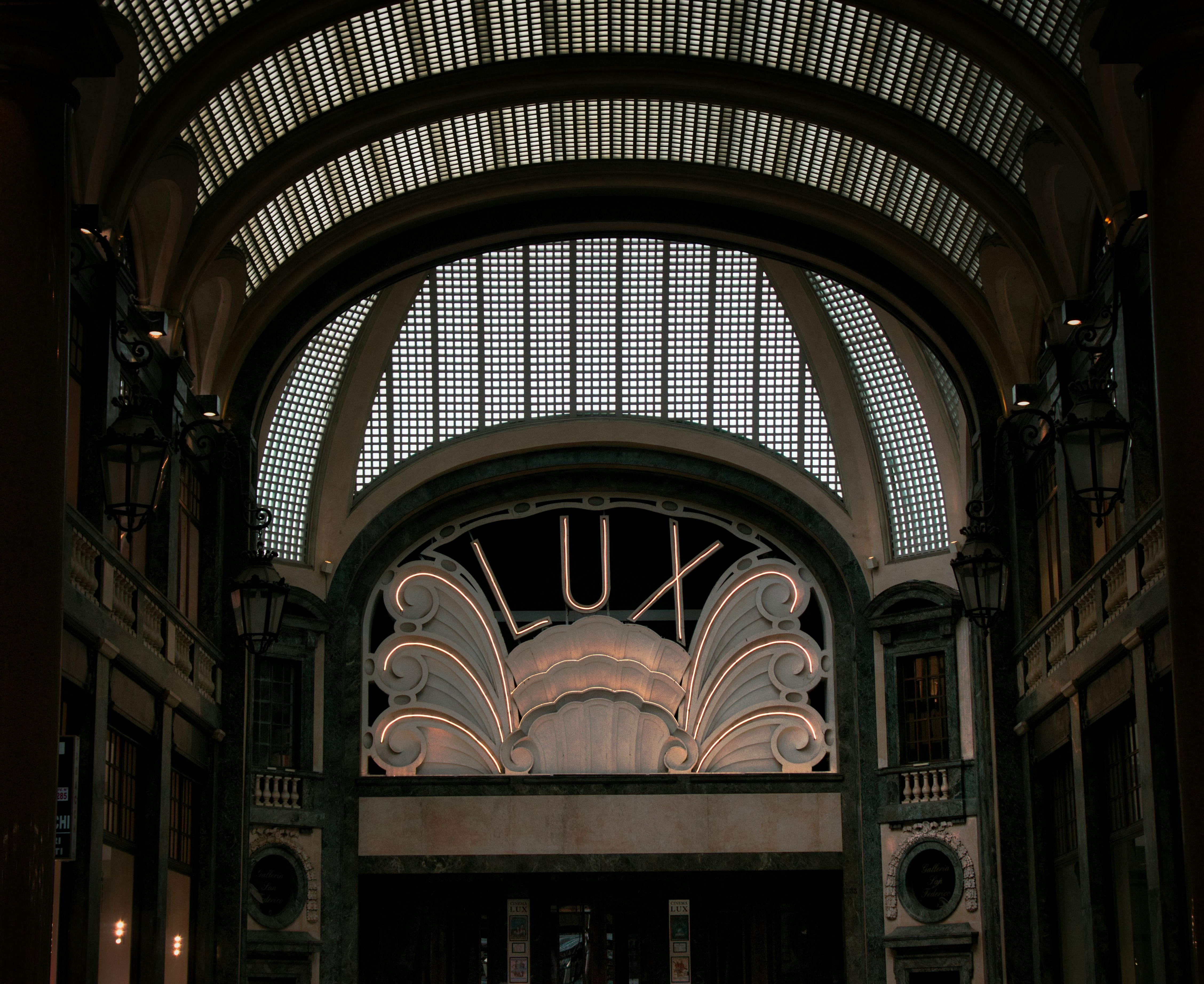 Interior of a grand building featuring an Art Deco sign reading 'LUX' under arched glass ceilings.