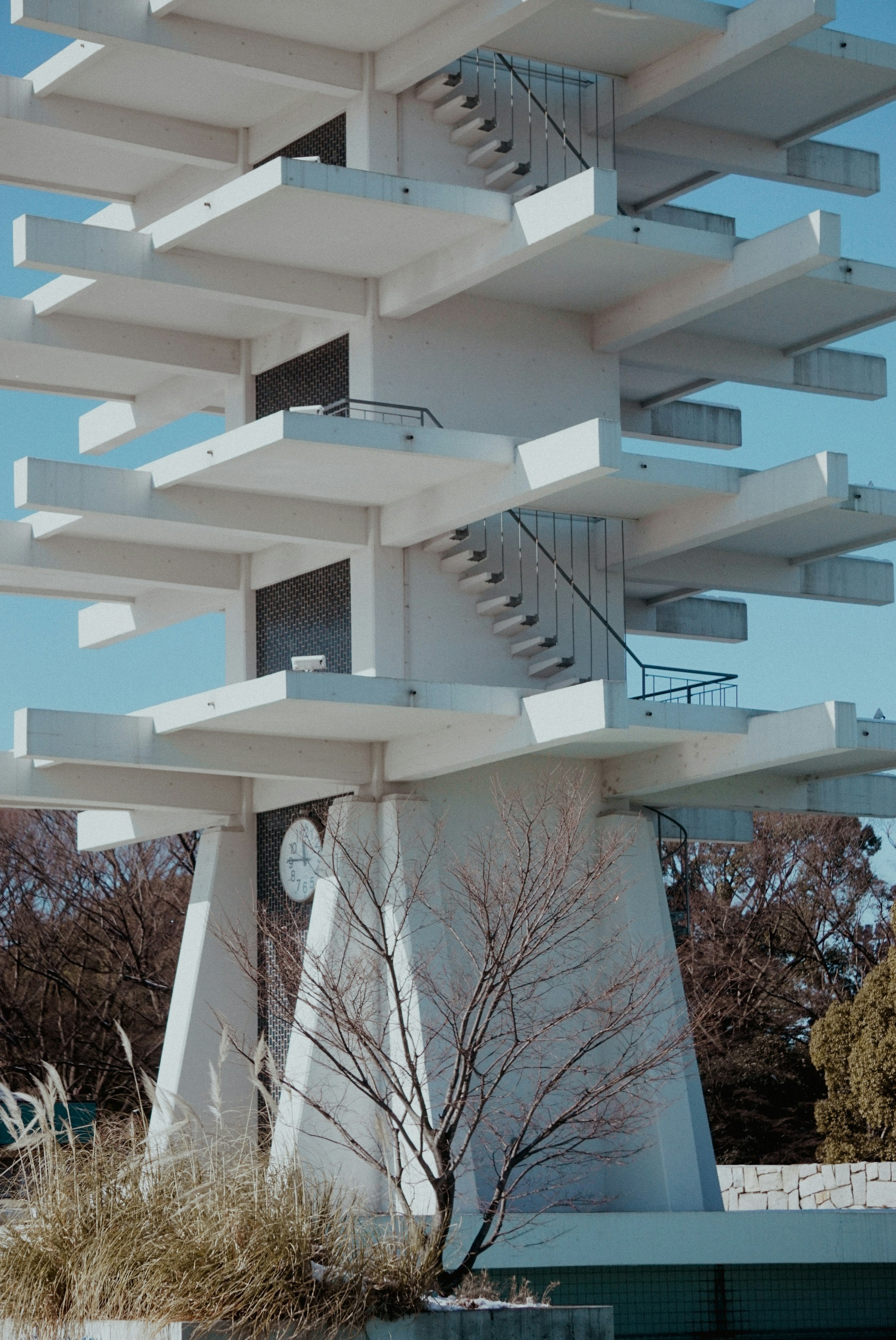 A contemporary pagoda structure with multiple levels and a clock, surrounded by minimalistic landscaping. The design emphasizes clean lines and geometric forms.