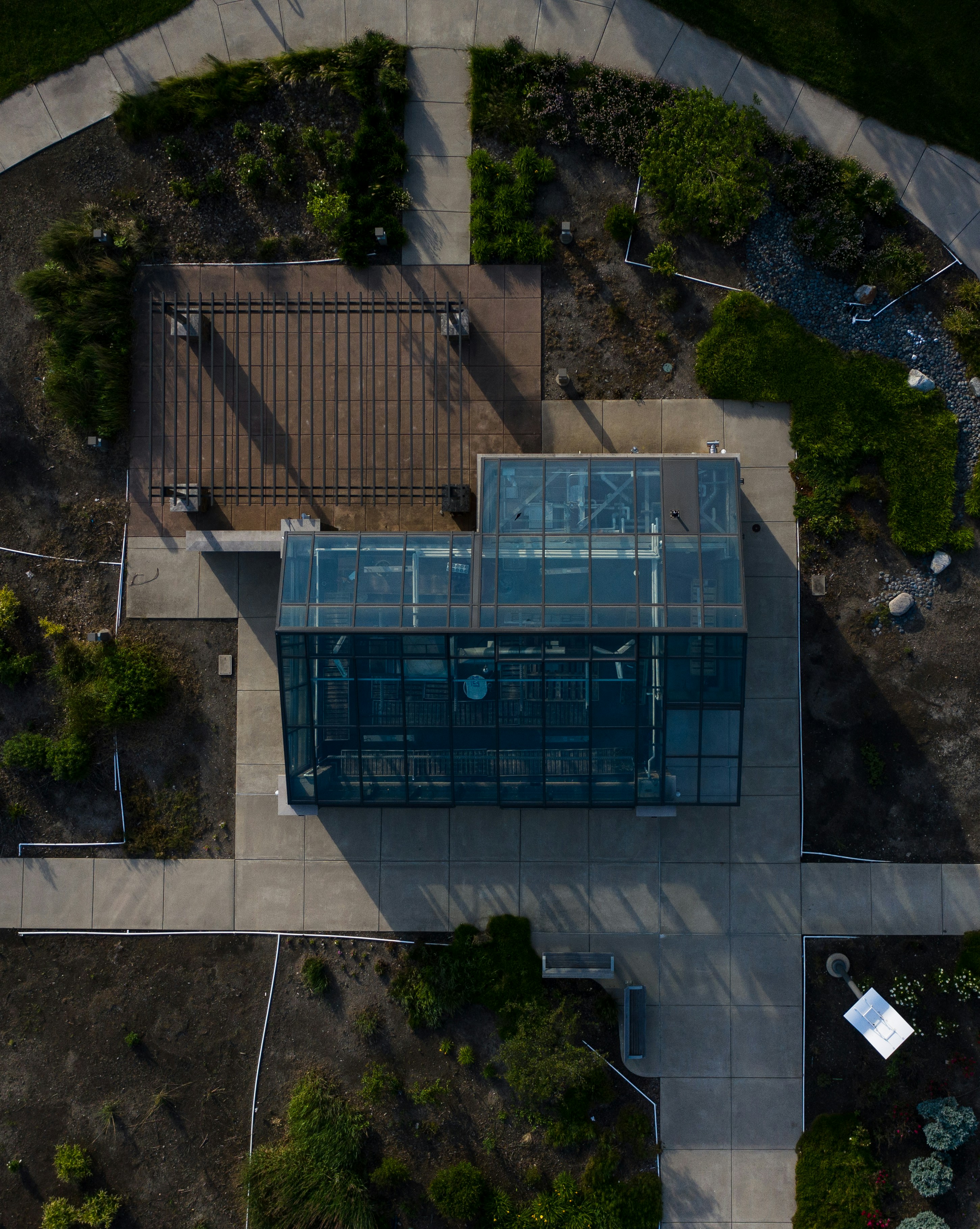 Aerial view of a glass greenhouse surrounded by neatly arranged pathways and lush greenery. The layout highlights the harmony of architecture and nature.