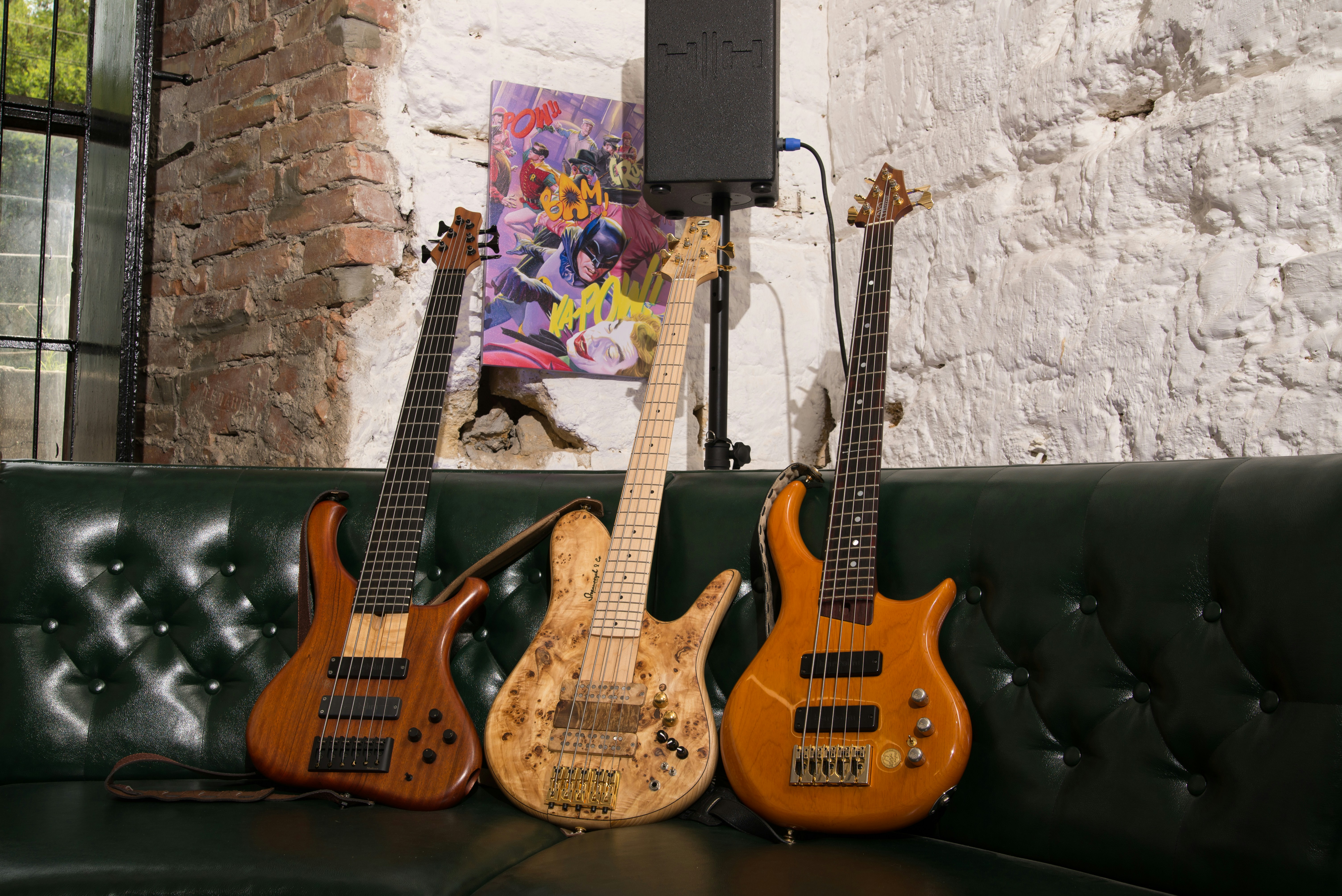 Guitars in repose: three basses glow against a brick-and-leather stage