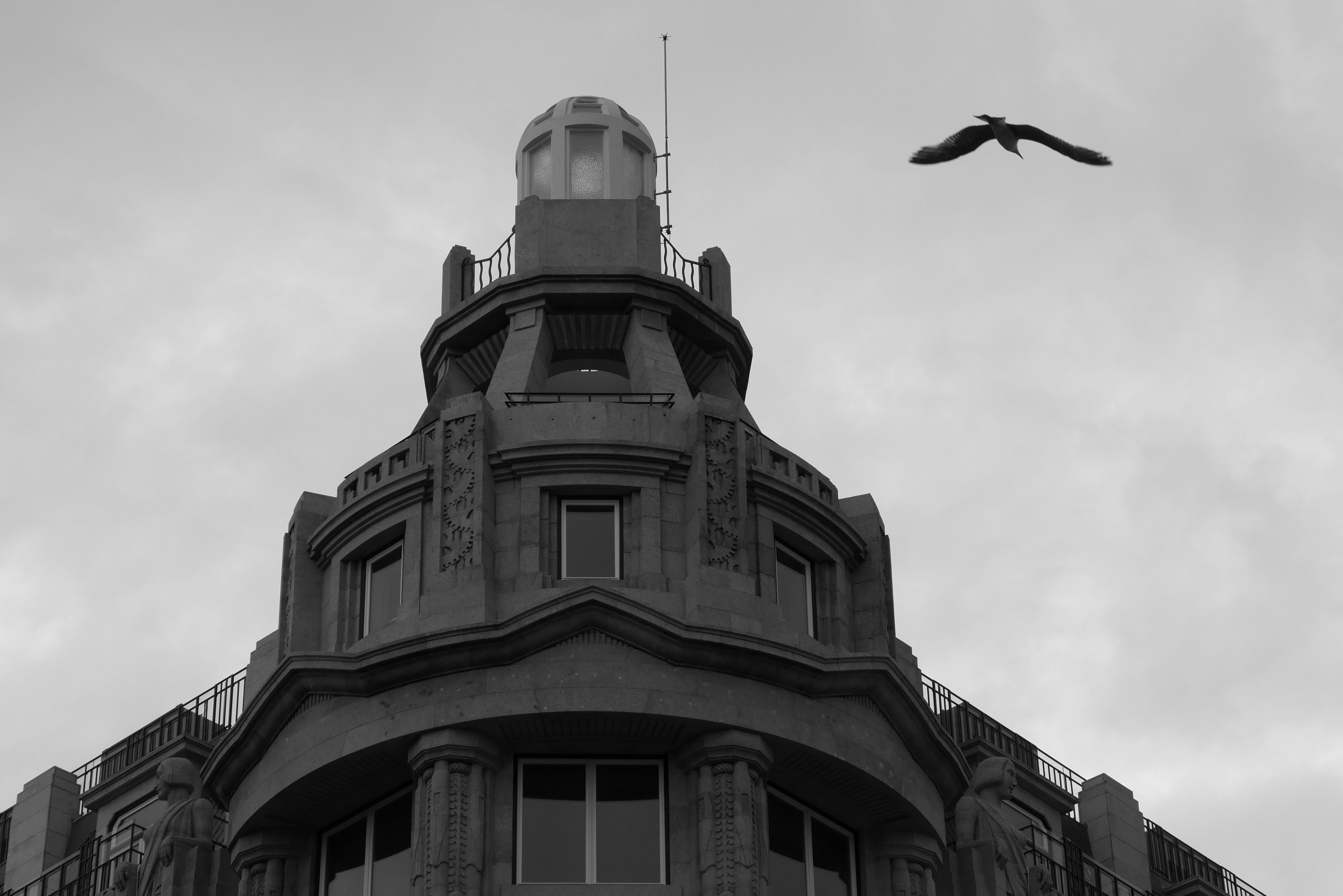 Monochrome Crown: Art Deco Turret and a Bird in Flight Against a Cloudy Sky