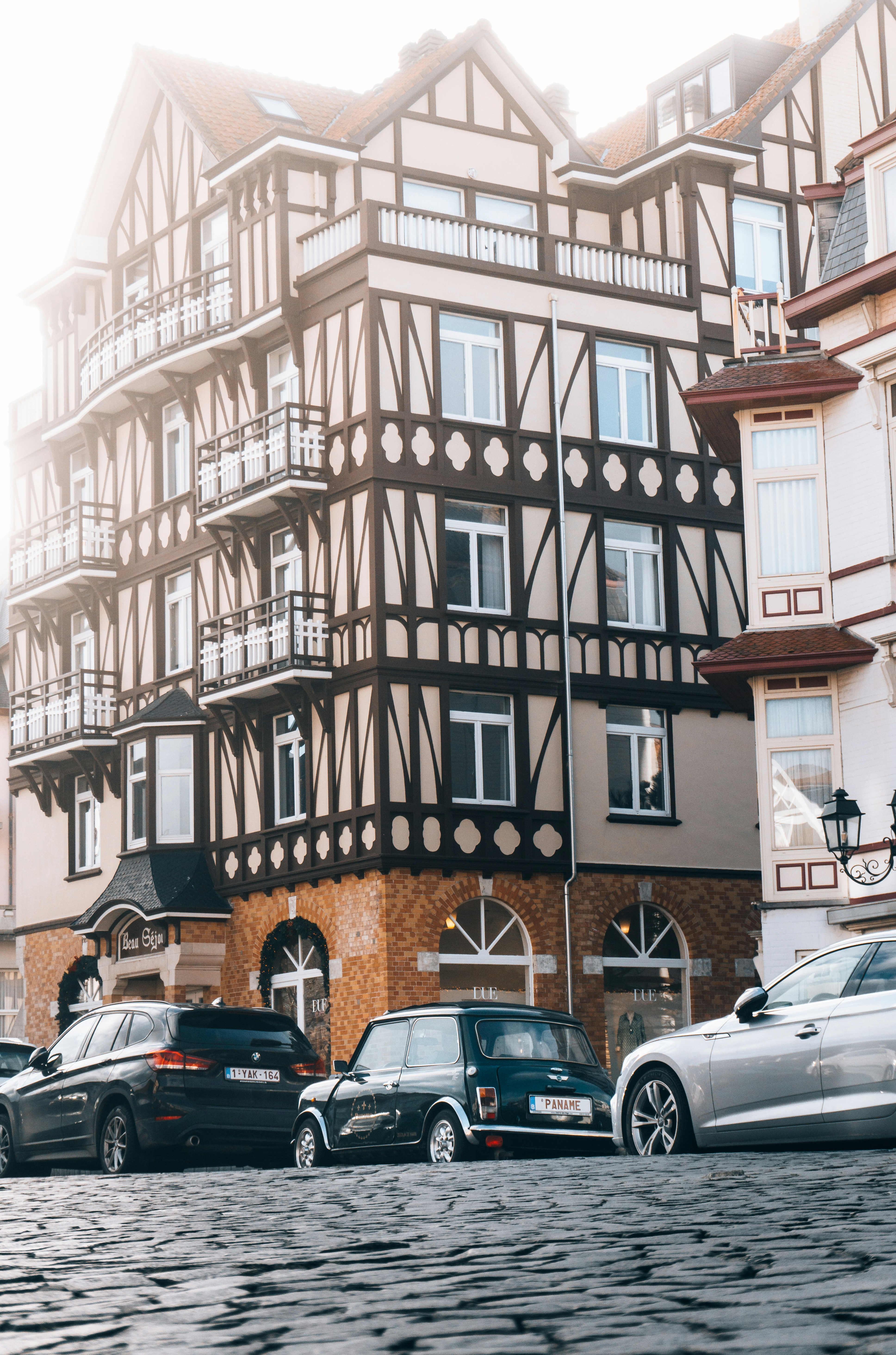 Tudor-style building with intricate patterns and modern cars on a cobblestone street.