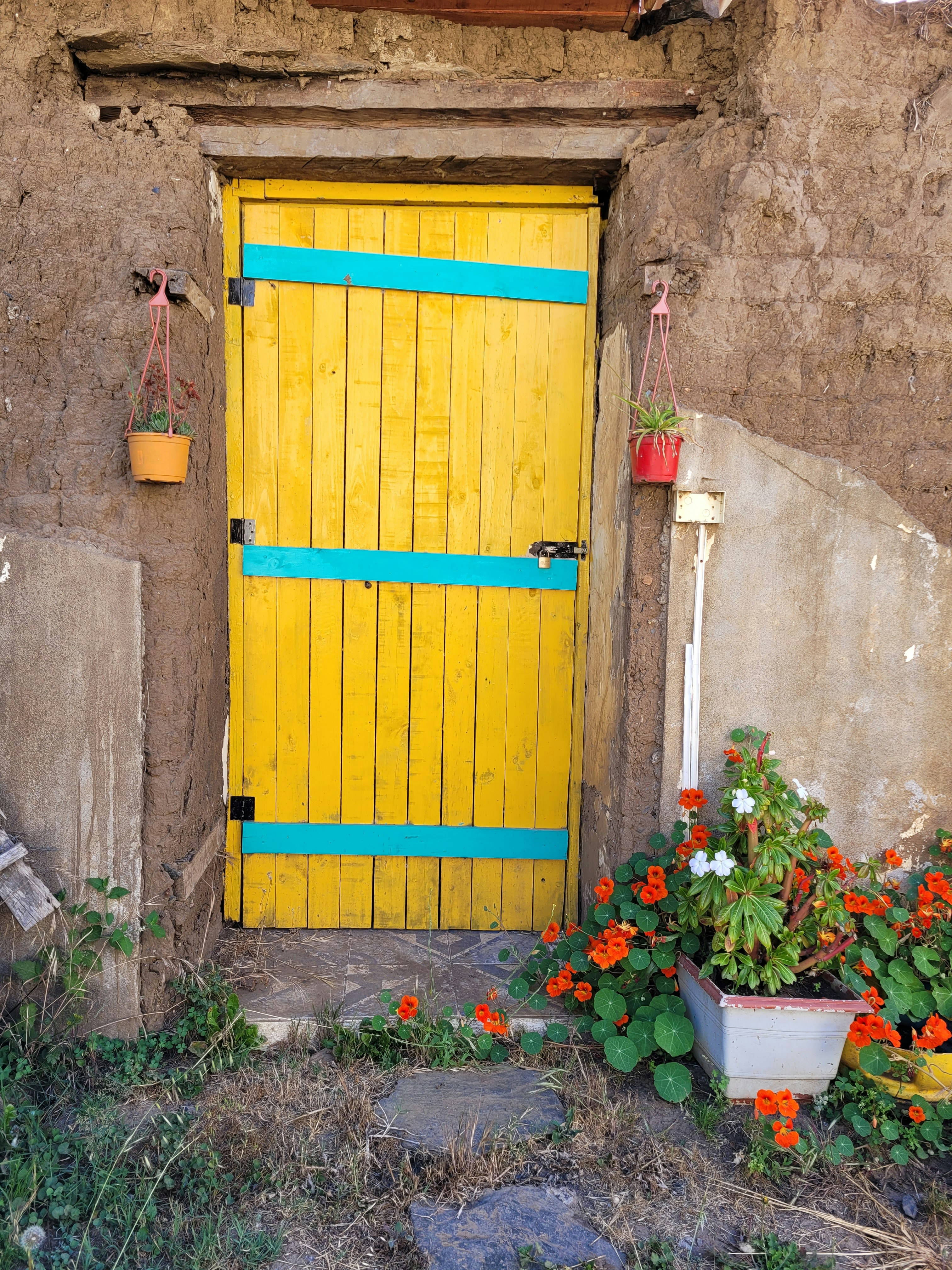 Yellow Door with Turquoise Straps: A Colorful Threshold in Earthen Walls