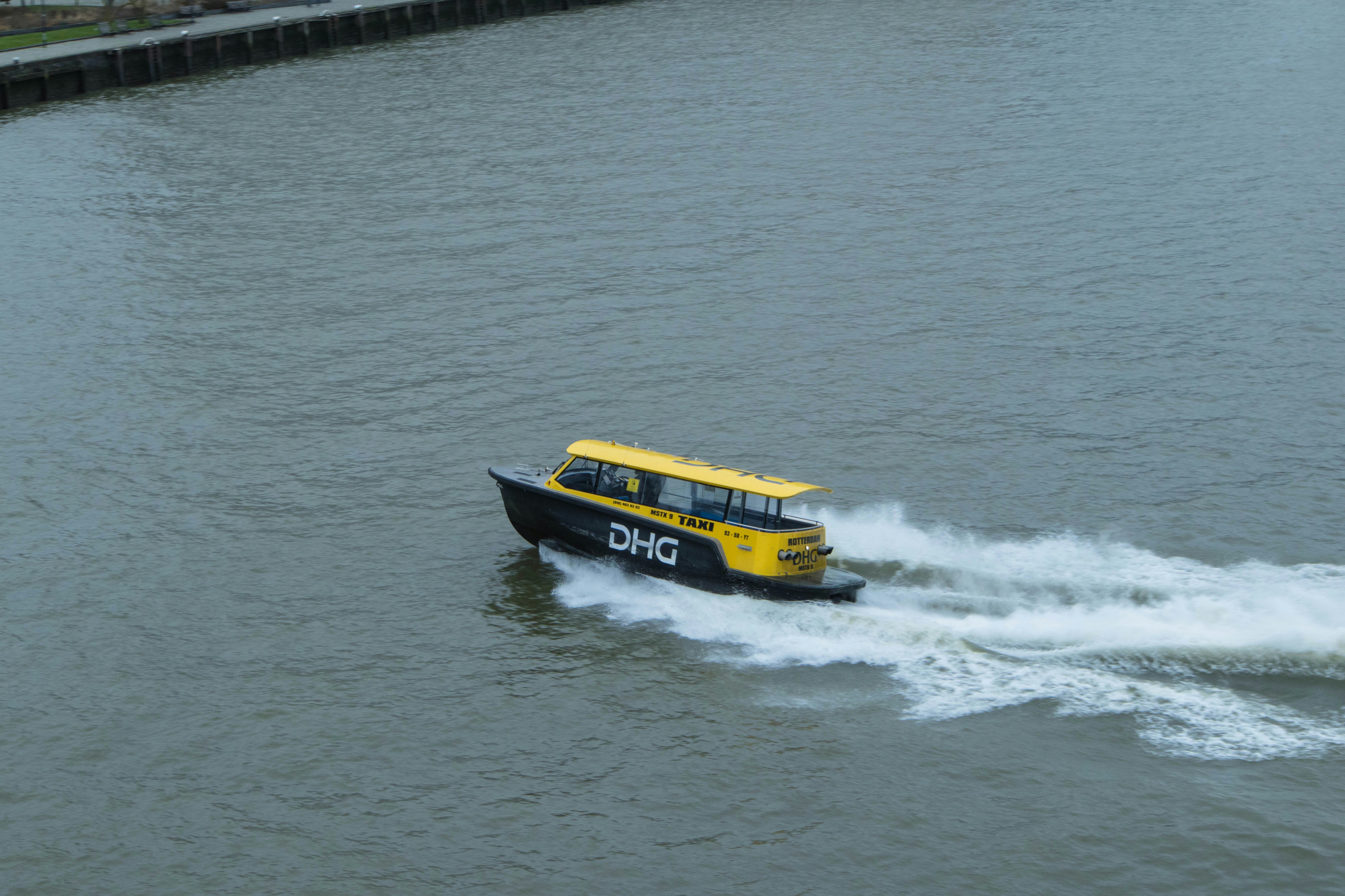 Neon-yellow DHG river taxi slices through a gray river, leaving a crisp white wake