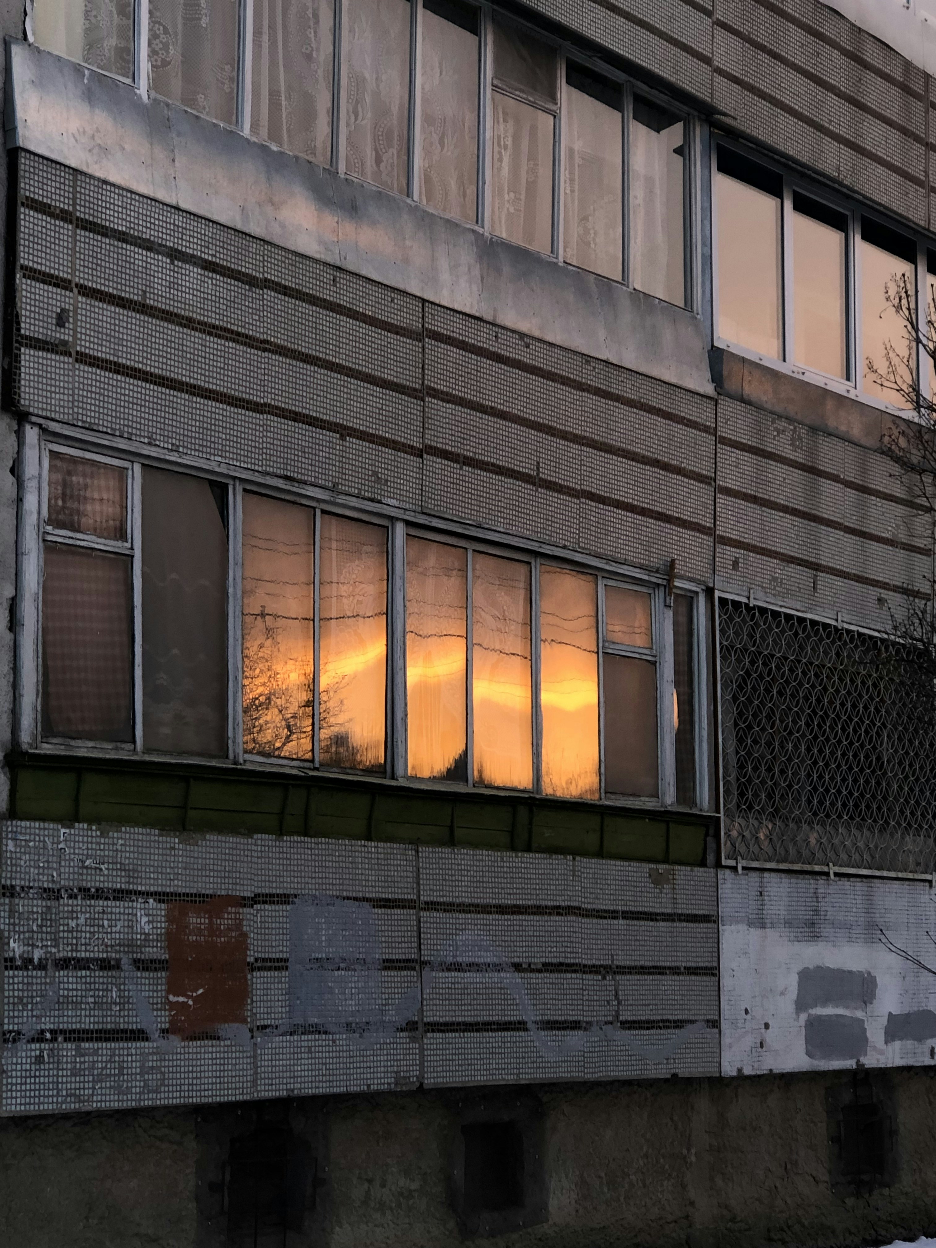 Warm sunset reflections shimmering in the windows of a weathered building, revealing the contrast between nature and urban decay.