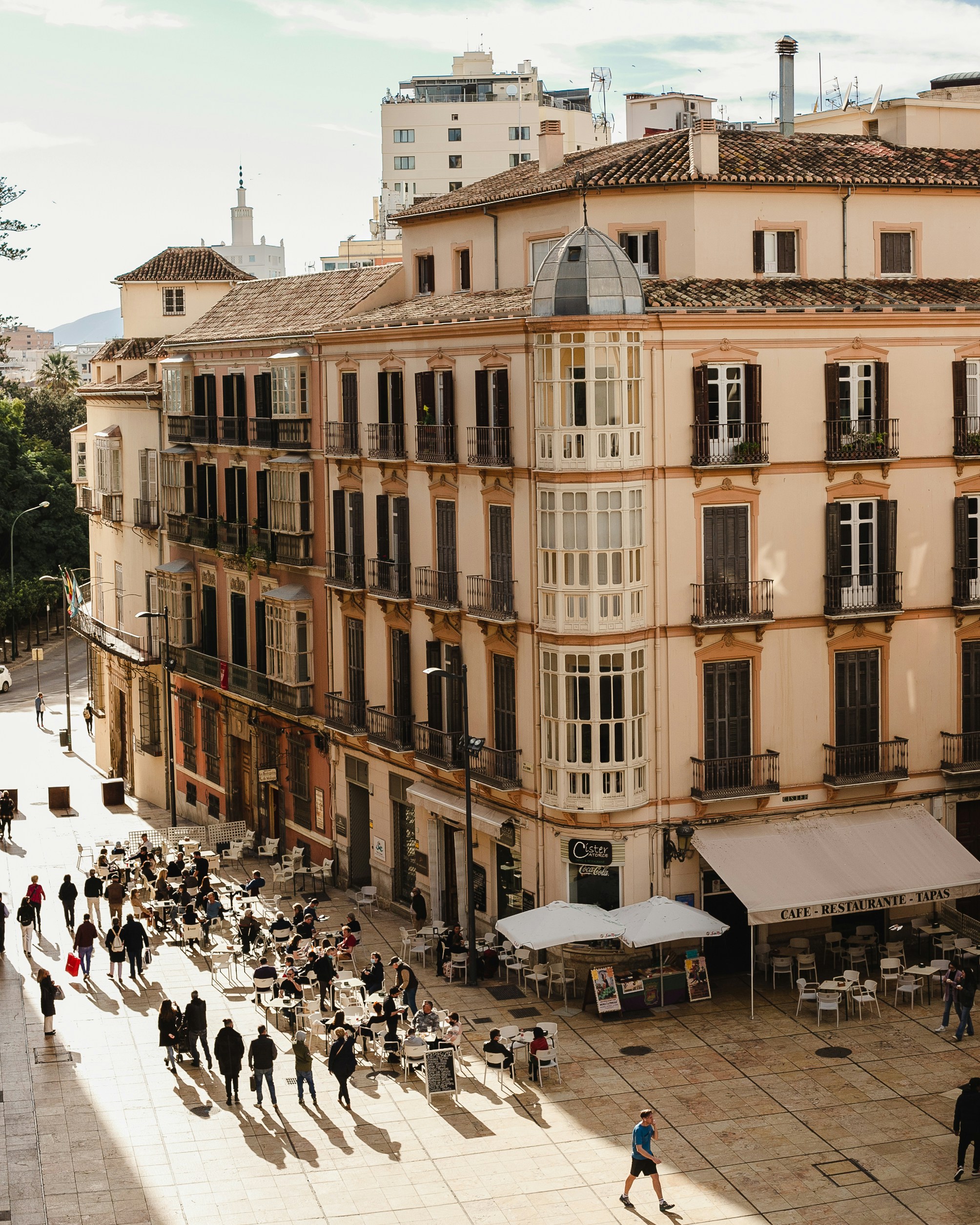 Charming street scene featuring people enjoying outdoor cafés beside historic buildings, with long shadows cast by the afternoon sun.