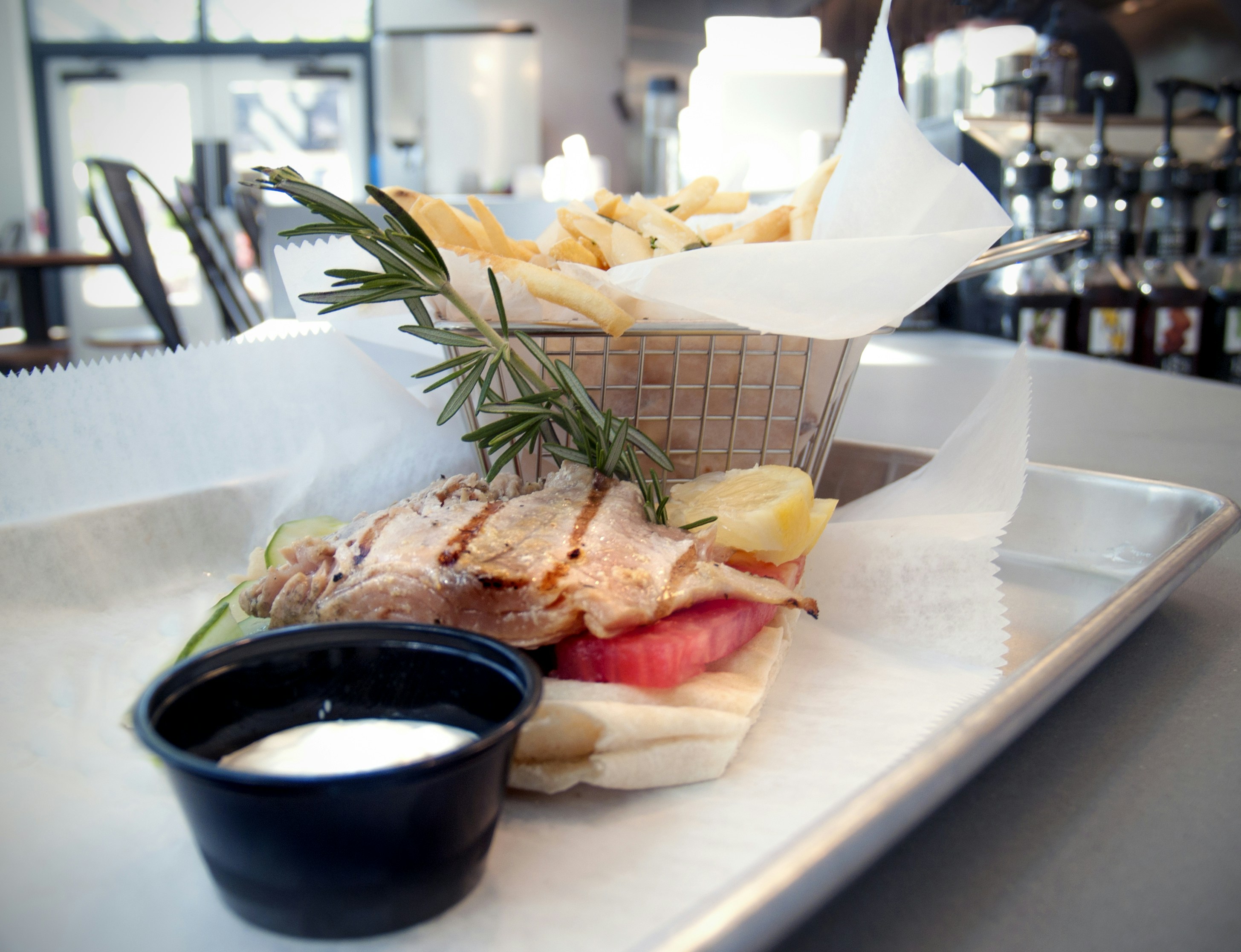 Grilled salmon garnished with rosemary, accompanied by fries in a cafe setting.