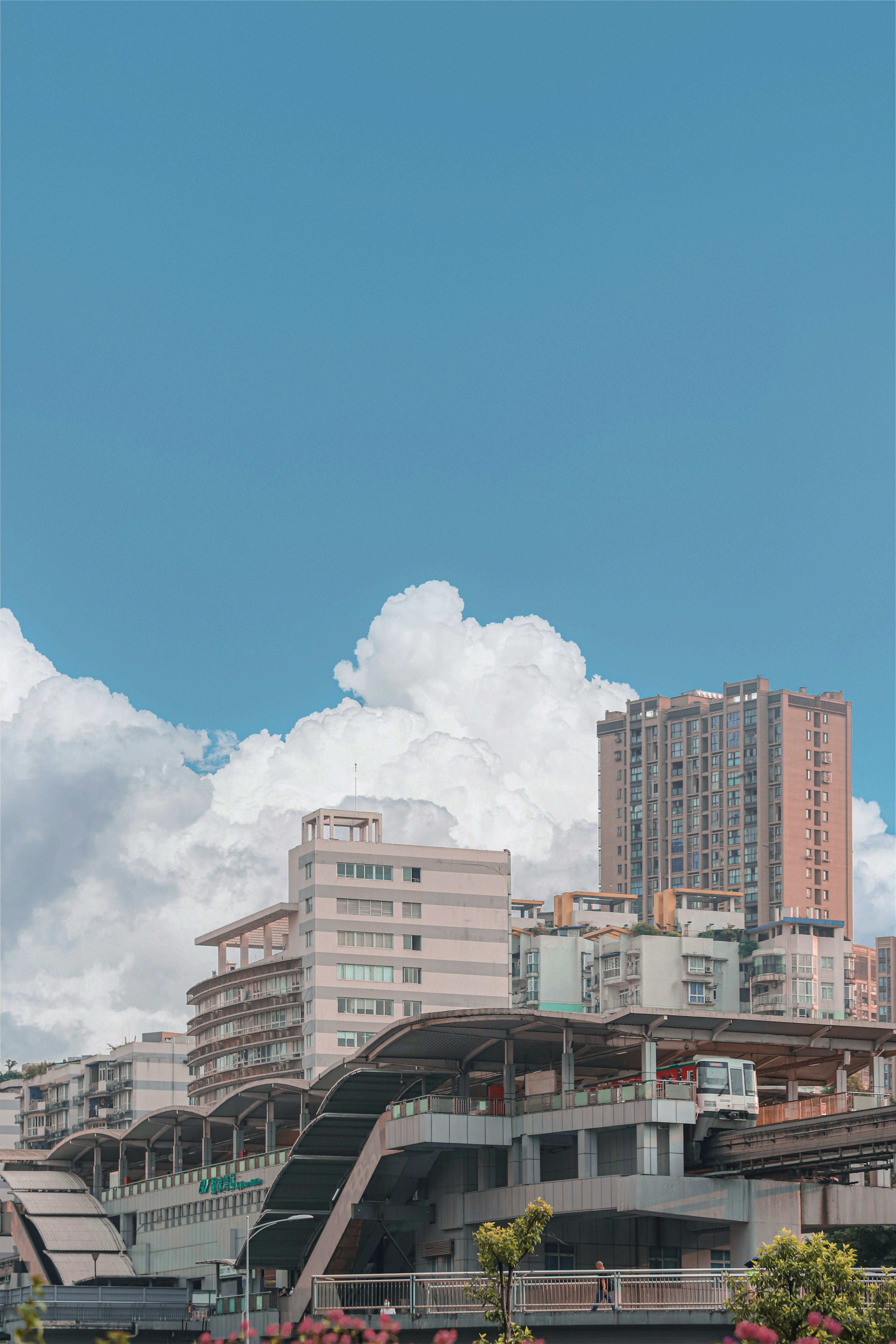 Modern transit station nestled among towering buildings under a clear blue sky, with fluffy clouds adding depth to the scene.