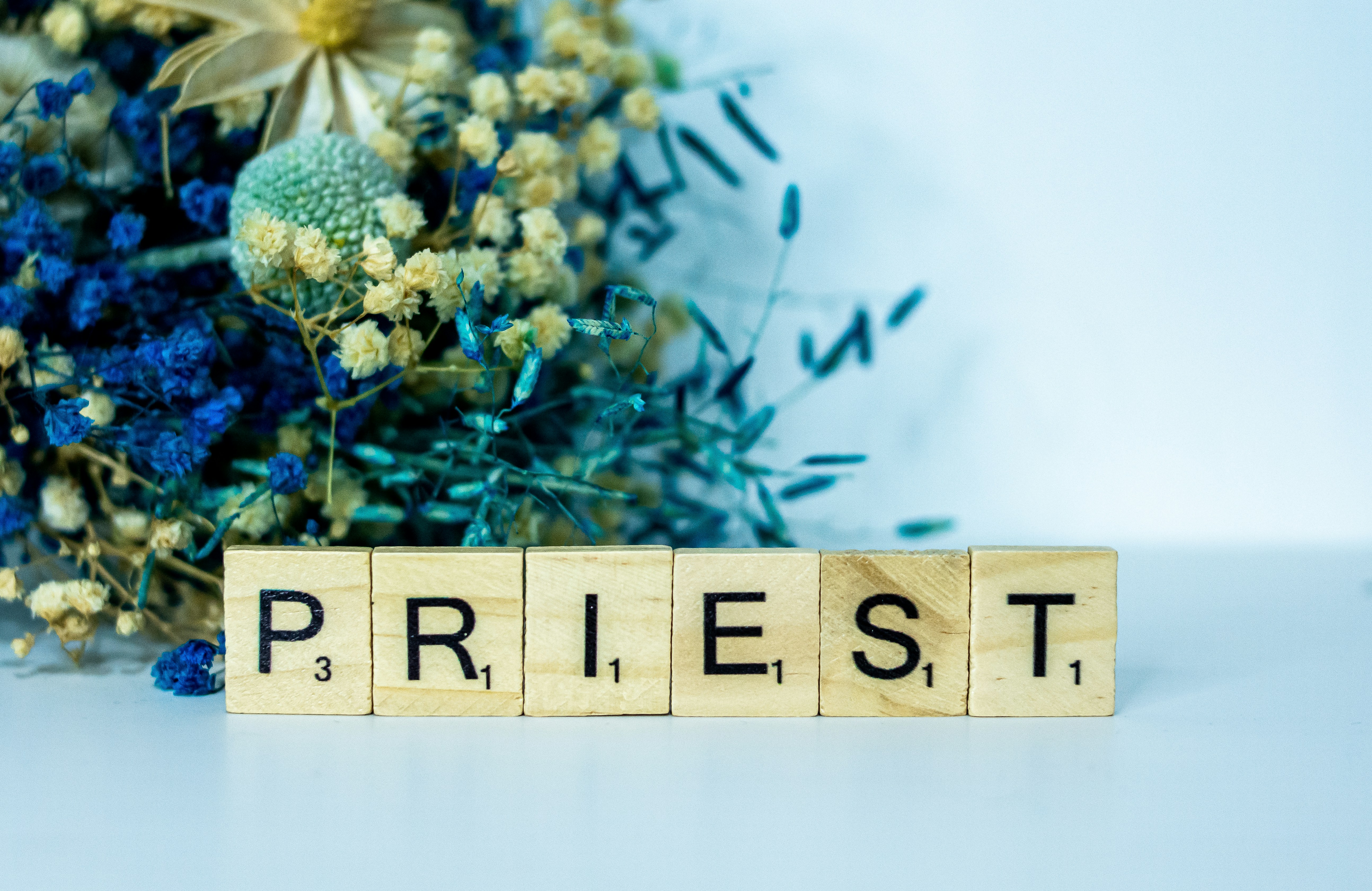 A wooden block spelling the word priest next to a bouquet of flowers ...