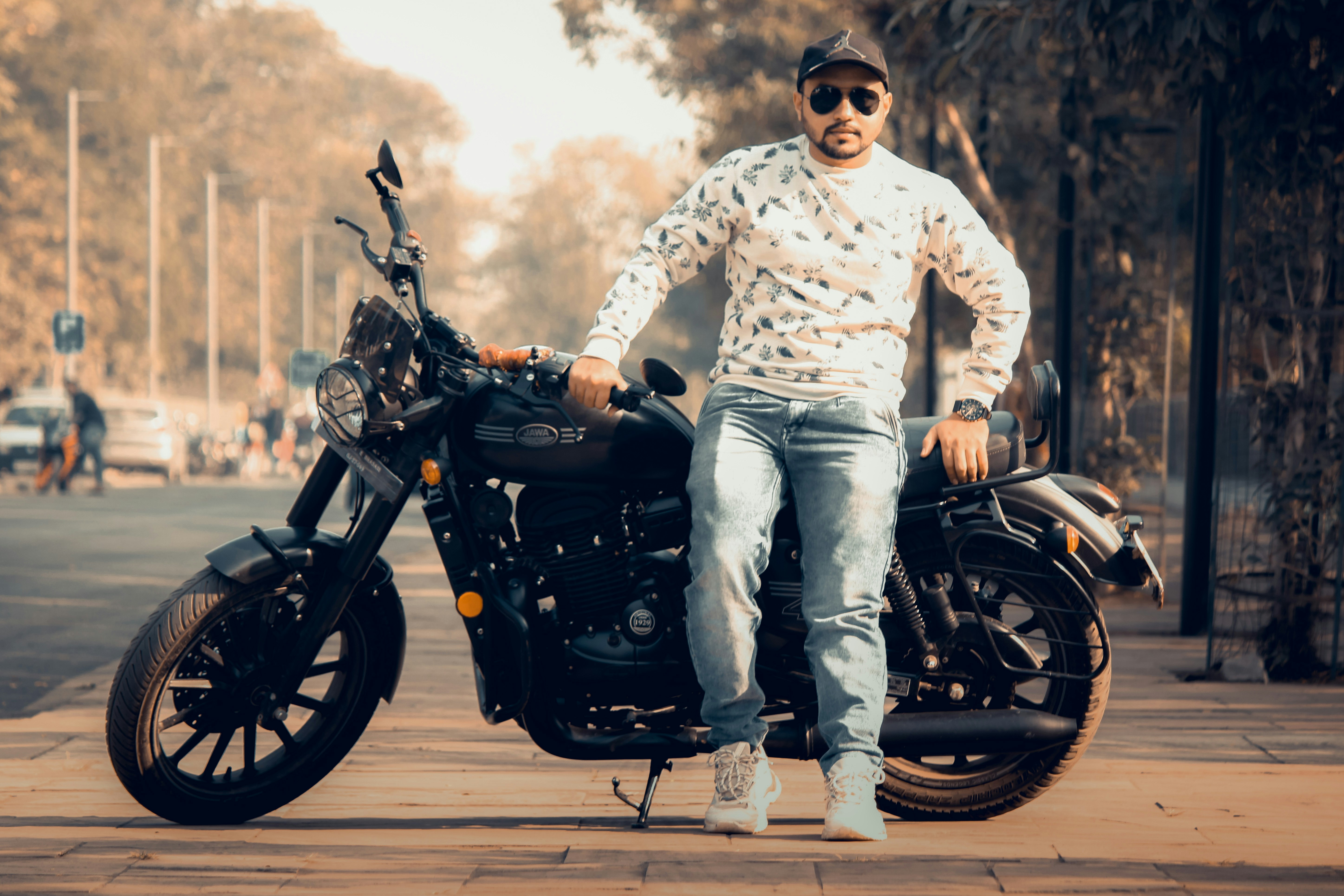 Man in casual attire leaning on a motorcycle in a sunlit urban setting.