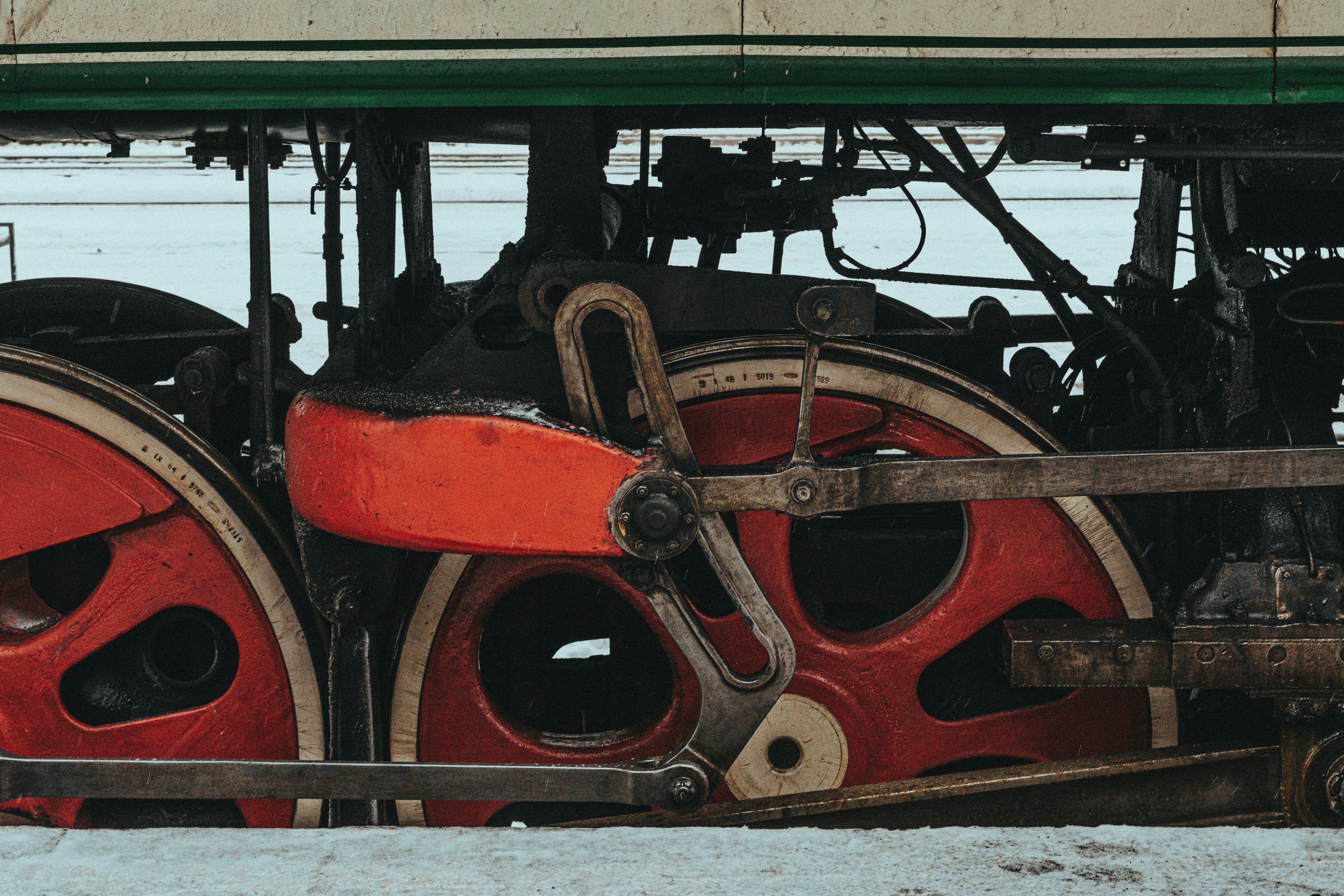 Close-up of the intricate mechanics of a vintage steam locomotive, highlighting the vibrant red wheels and connecting rods. The image showcases the engineering brilliance of historical trains.