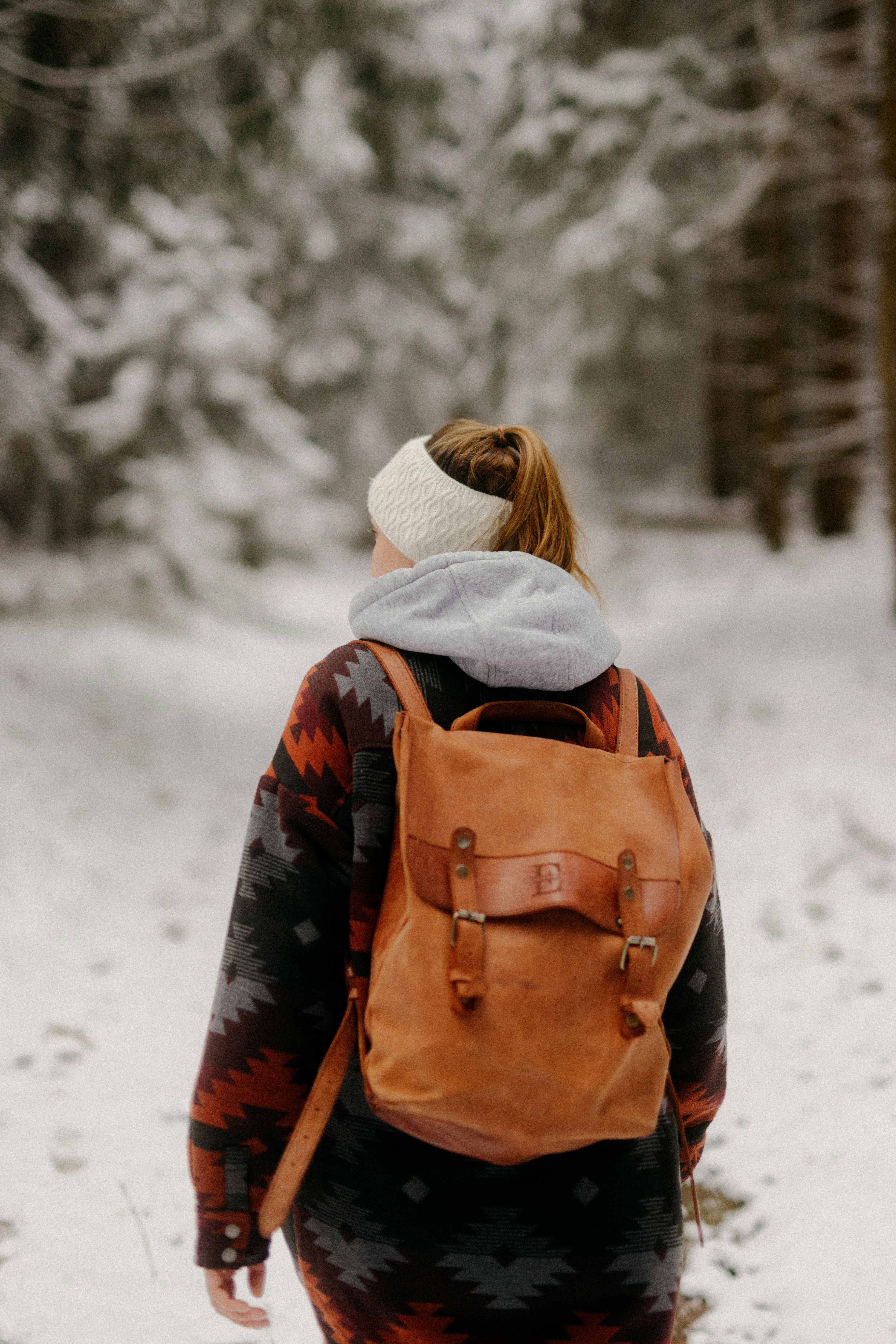 Person with a leather backpack walking through a snow-covered forest trail.