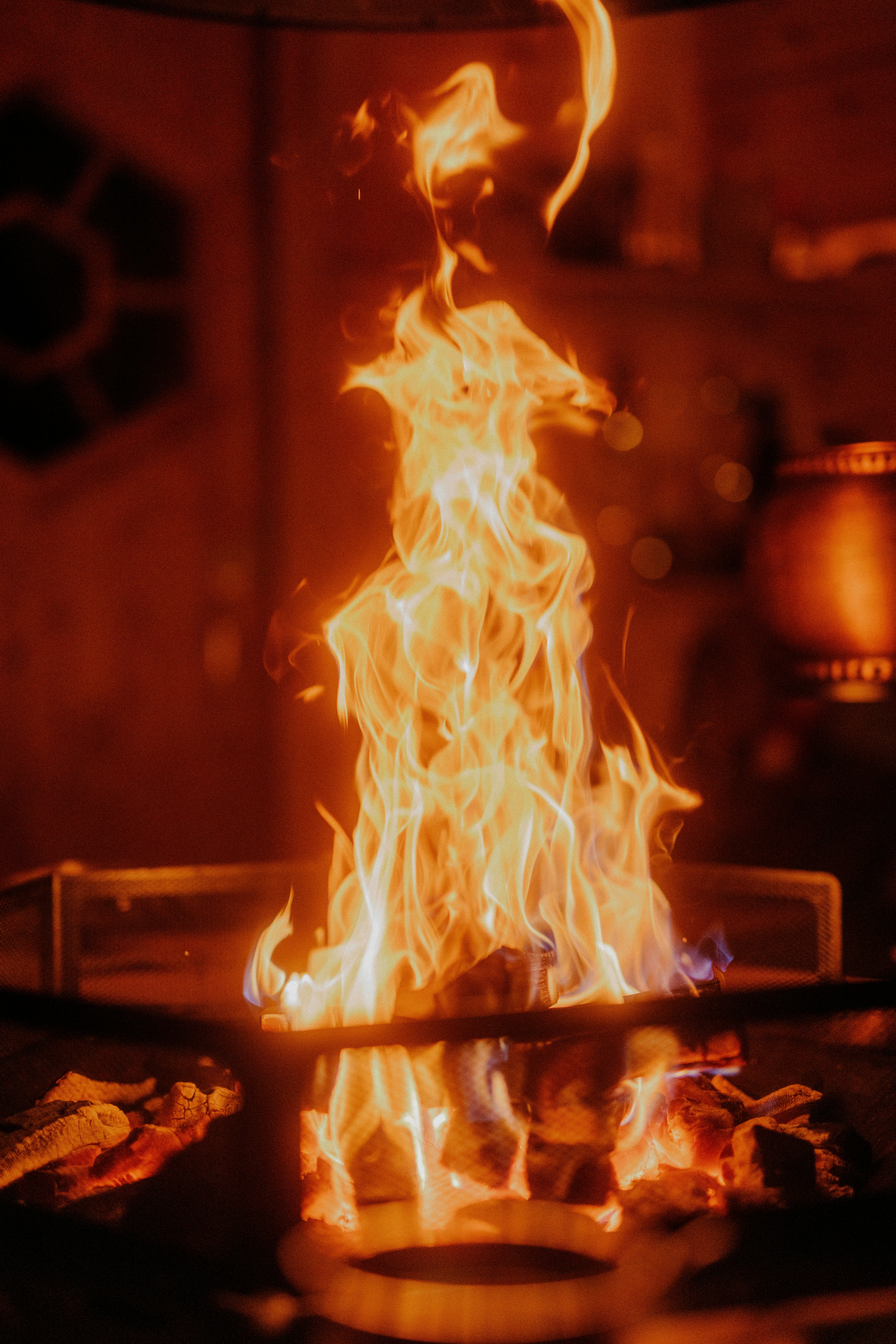 Vibrant flames rise from a fireplace in a dimly lit room, casting a warm, orange glow.