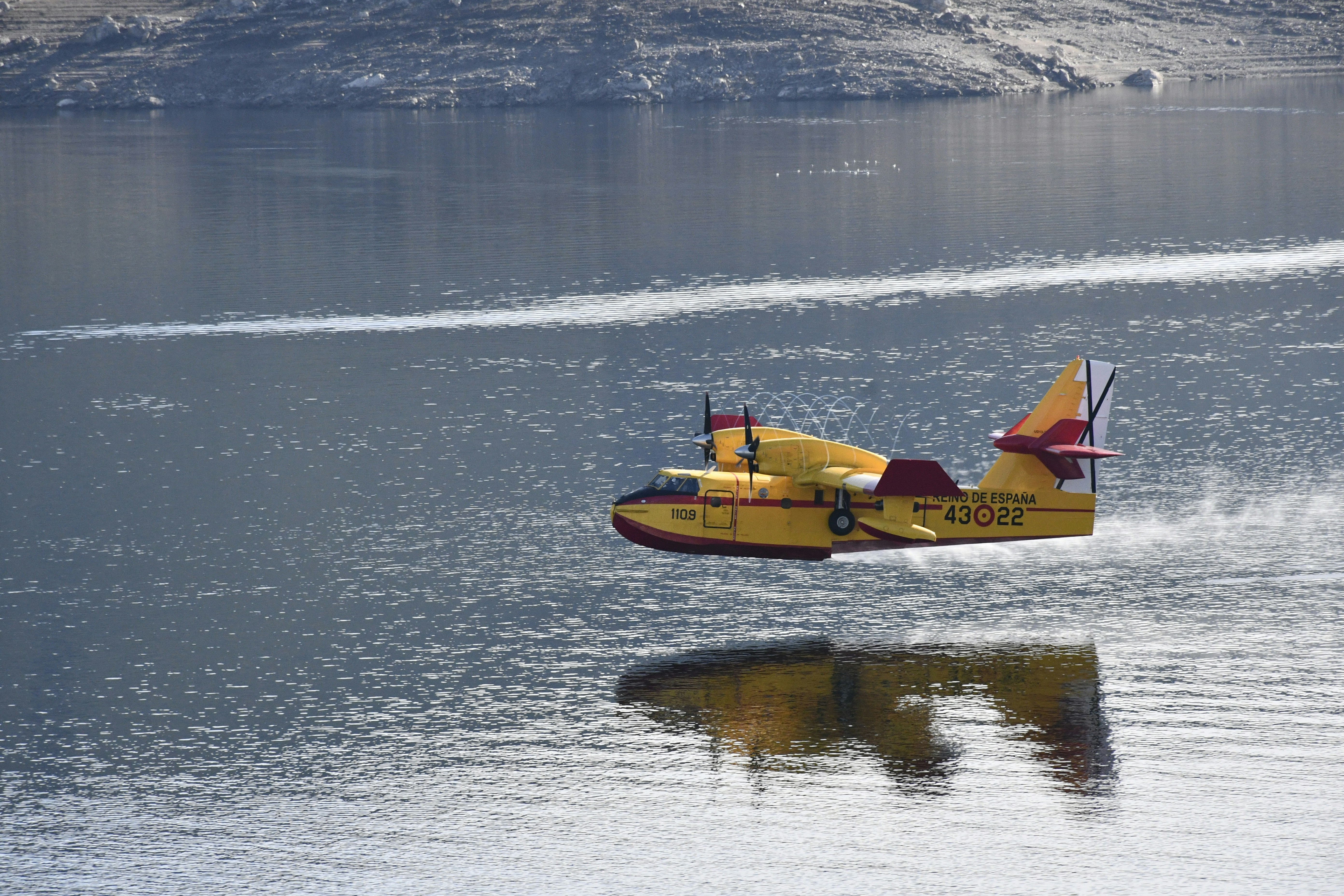 A small yellow plane flying over a body of water photo – Free Embalse ...