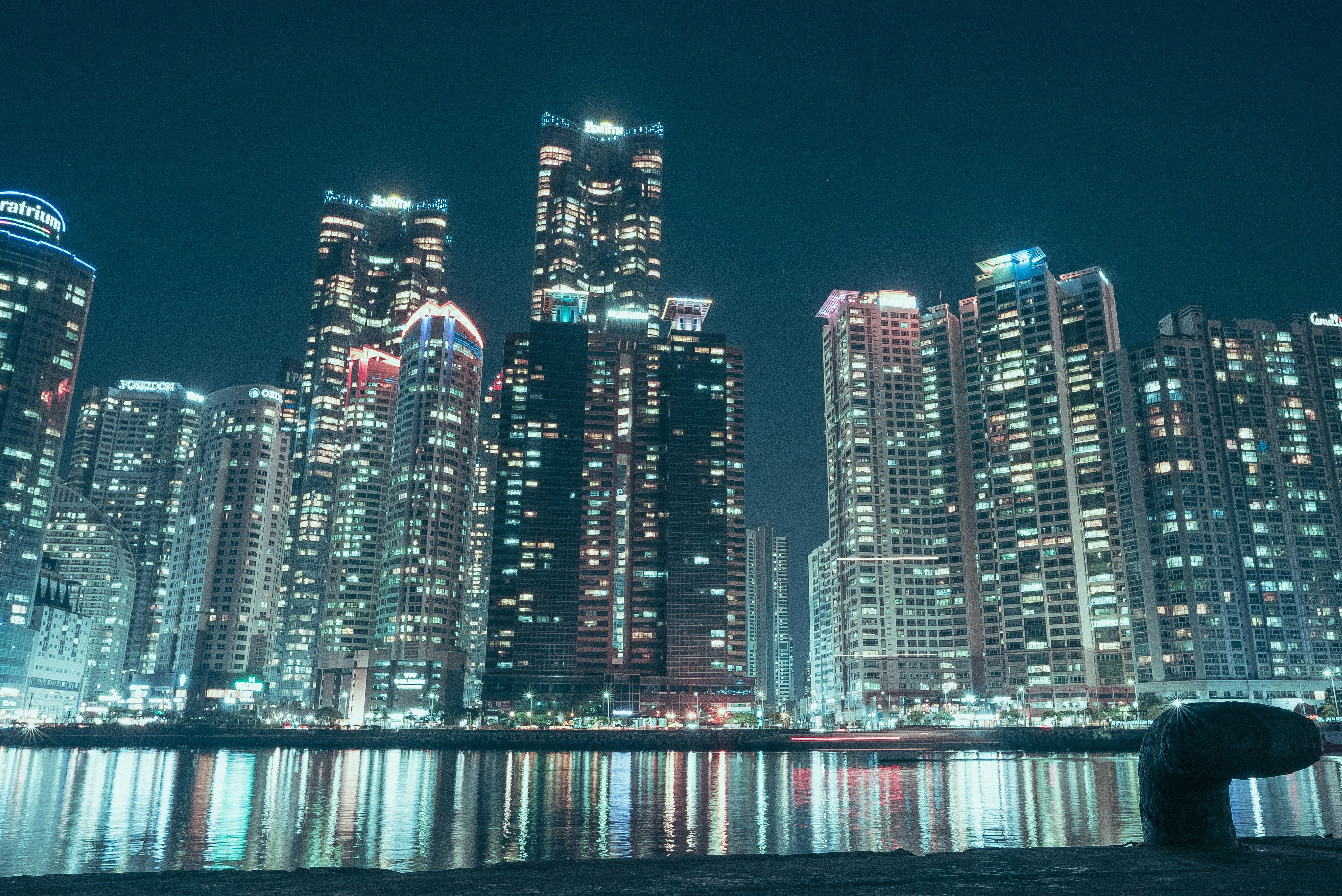 Vibrant city skyline illuminated by colorful lights reflecting on the water at night.