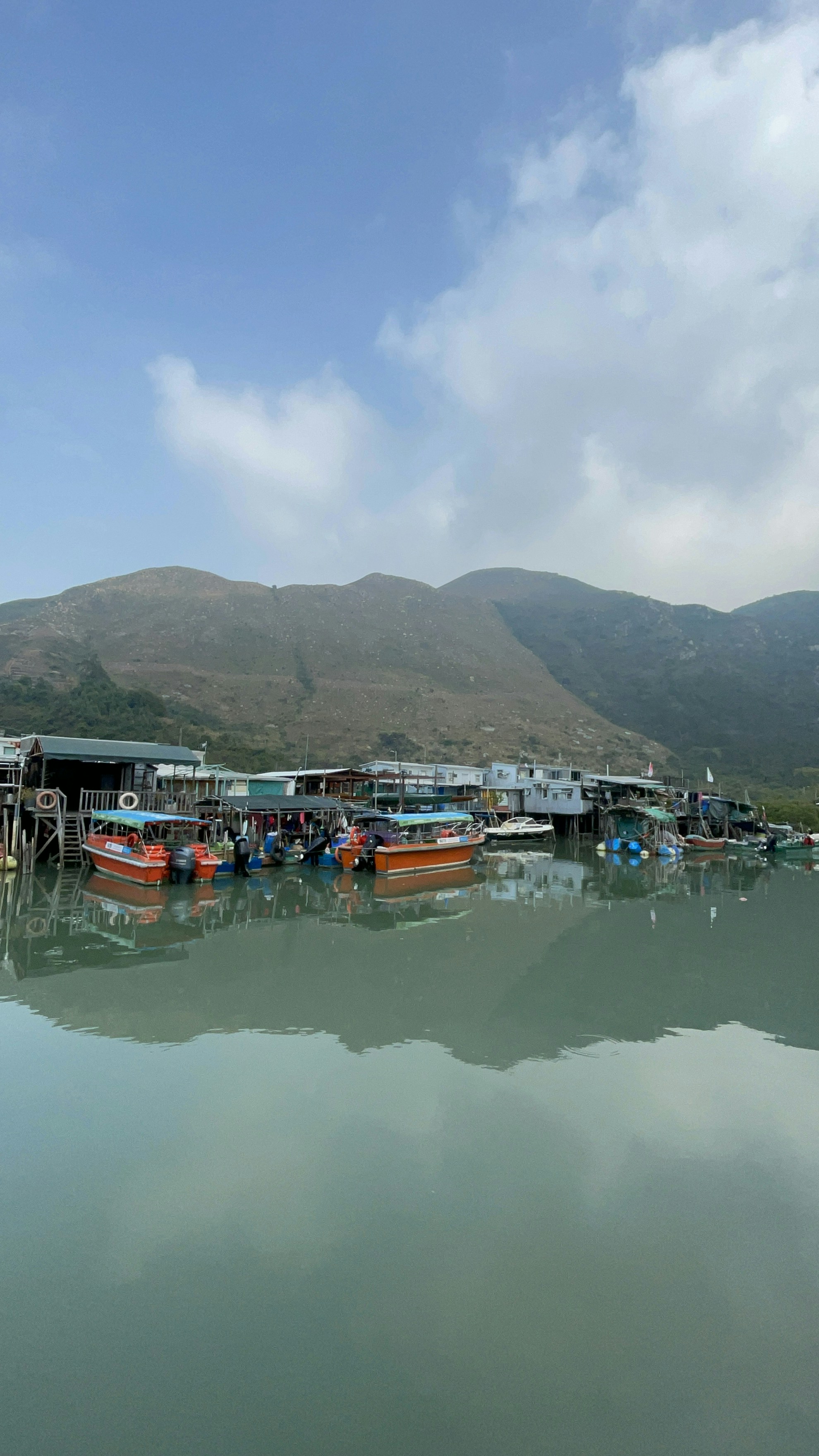 Boats at a hillside harbor, mirrored in tranquil water