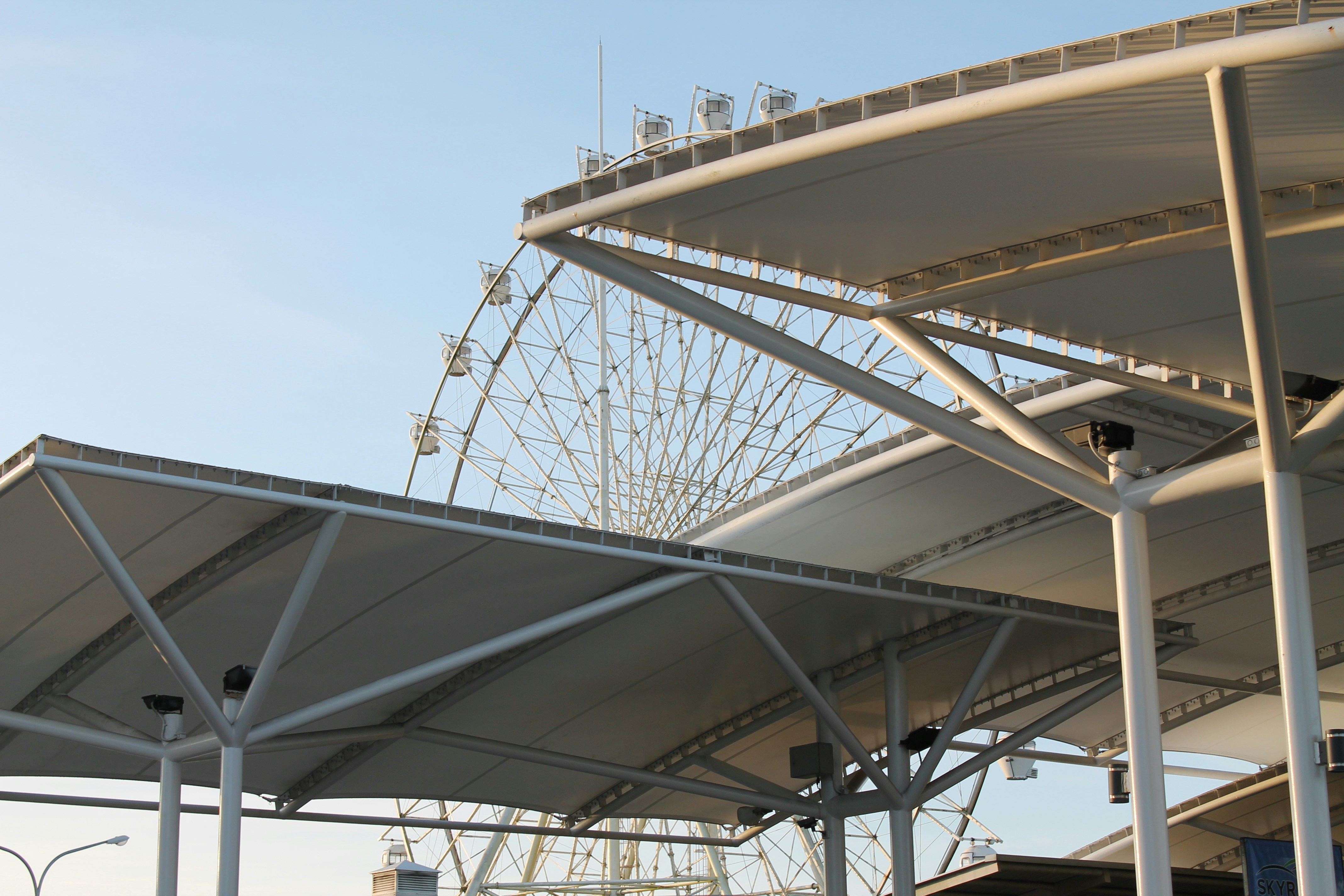 Ferris wheel peeking through architectural canopies in an urban setting during golden hour.