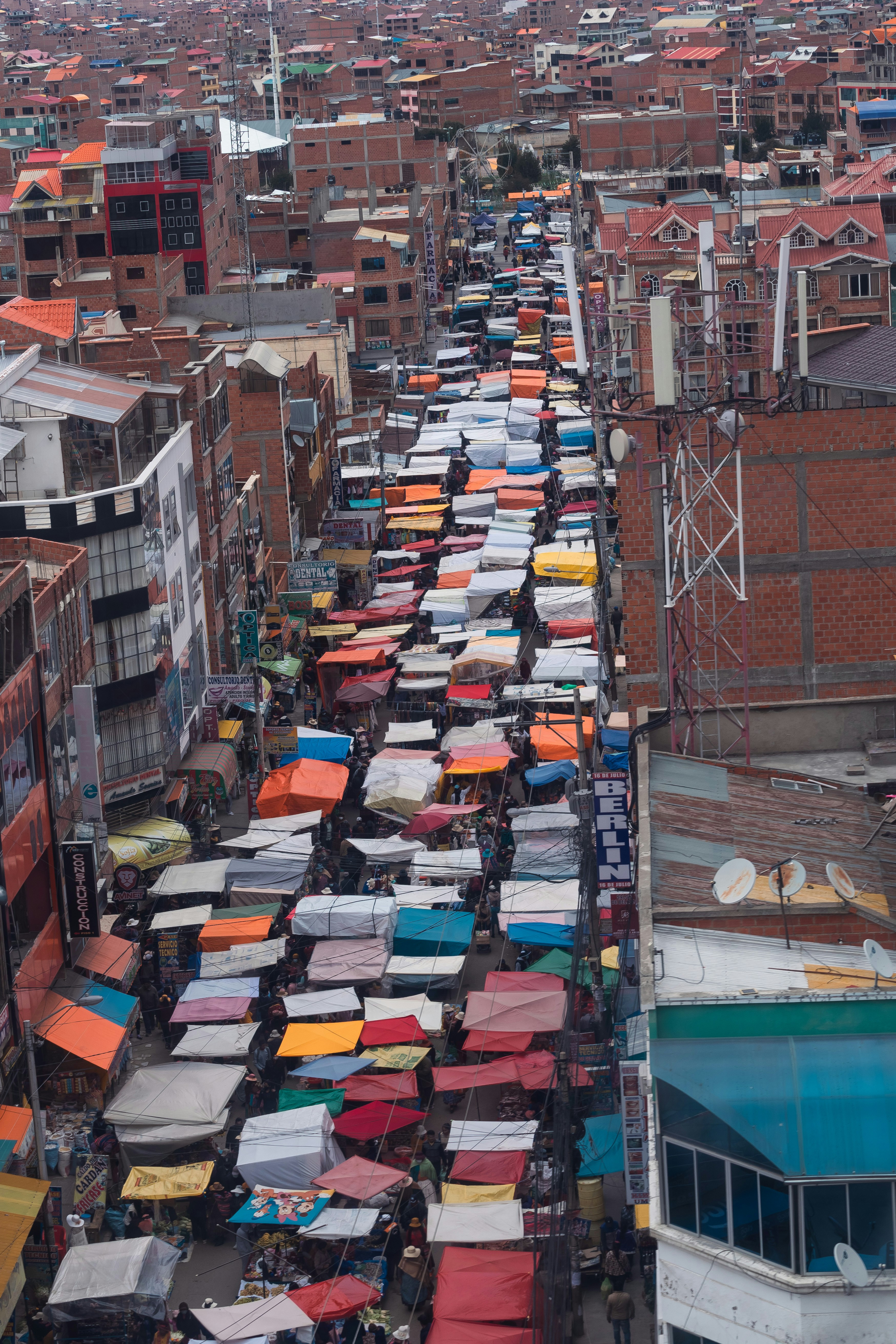 A bustling street market in an urban setting, filled with colorful tarps and busy vendors. The scene captures the lively atmosphere of daily commerce.