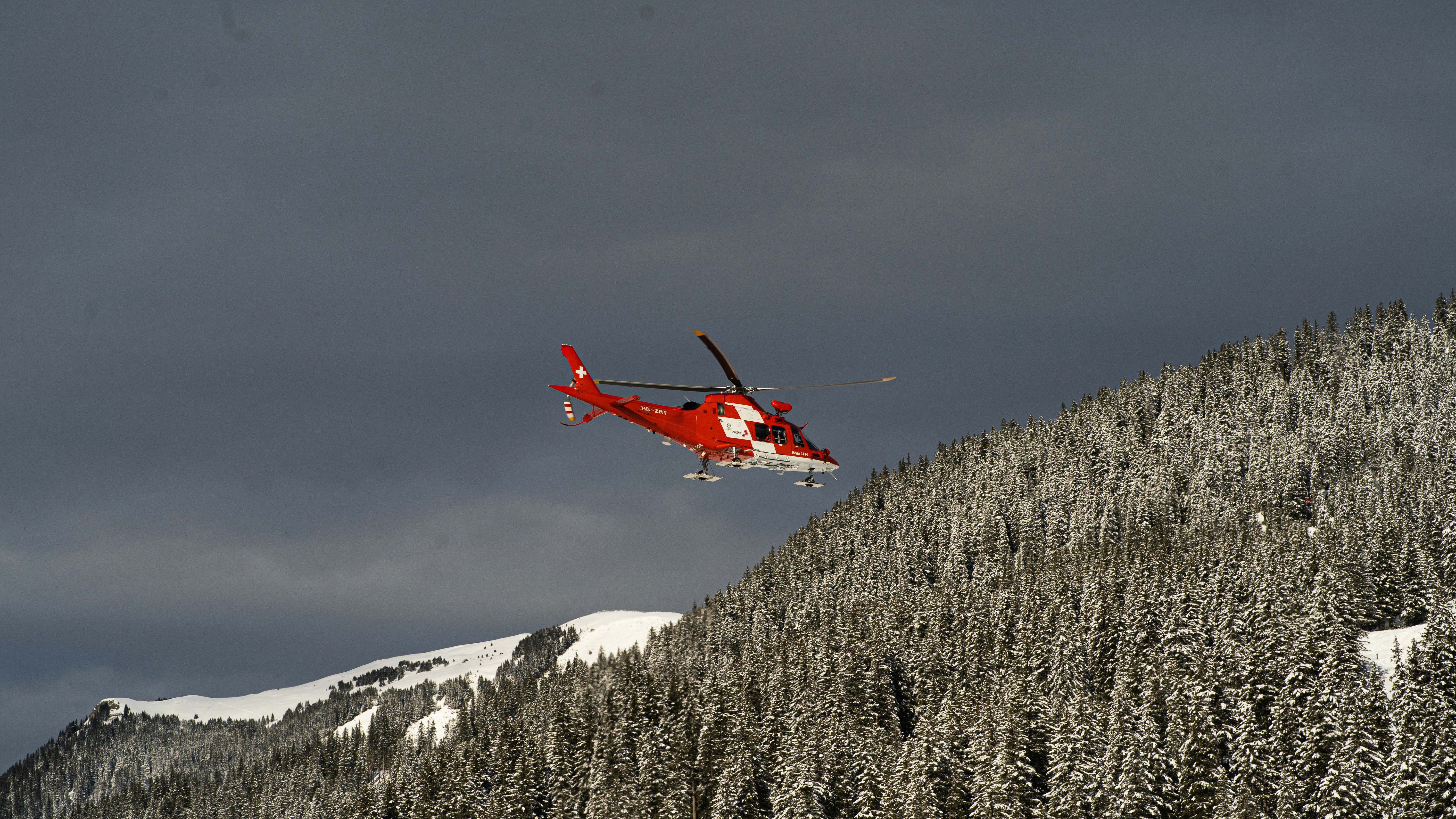 A red helicopter flying over a snow covered mountain photo – Free ...