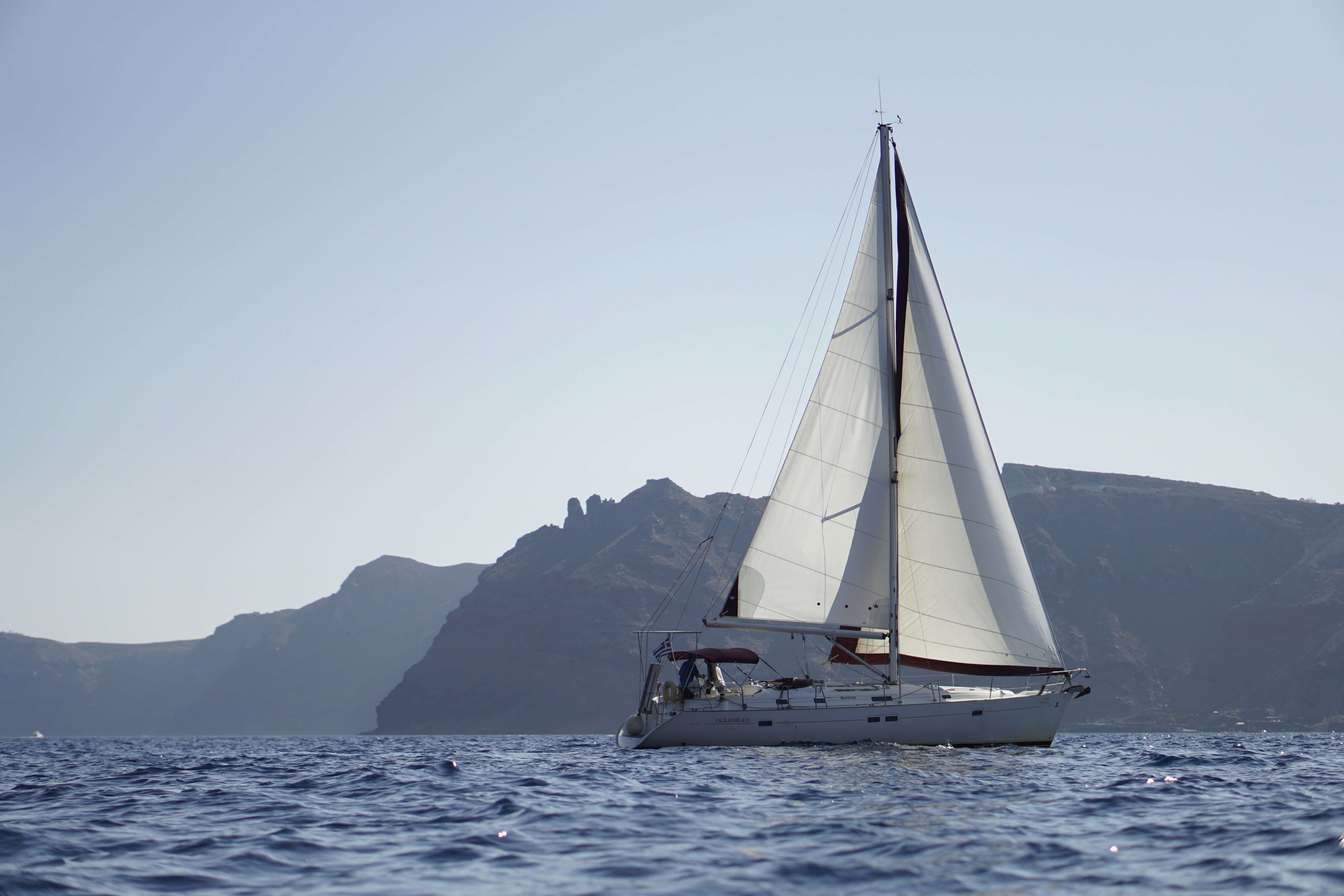 Foto zum Thema Ein Segelboot, das im Ozean mit Bergen im Hintergrund ...