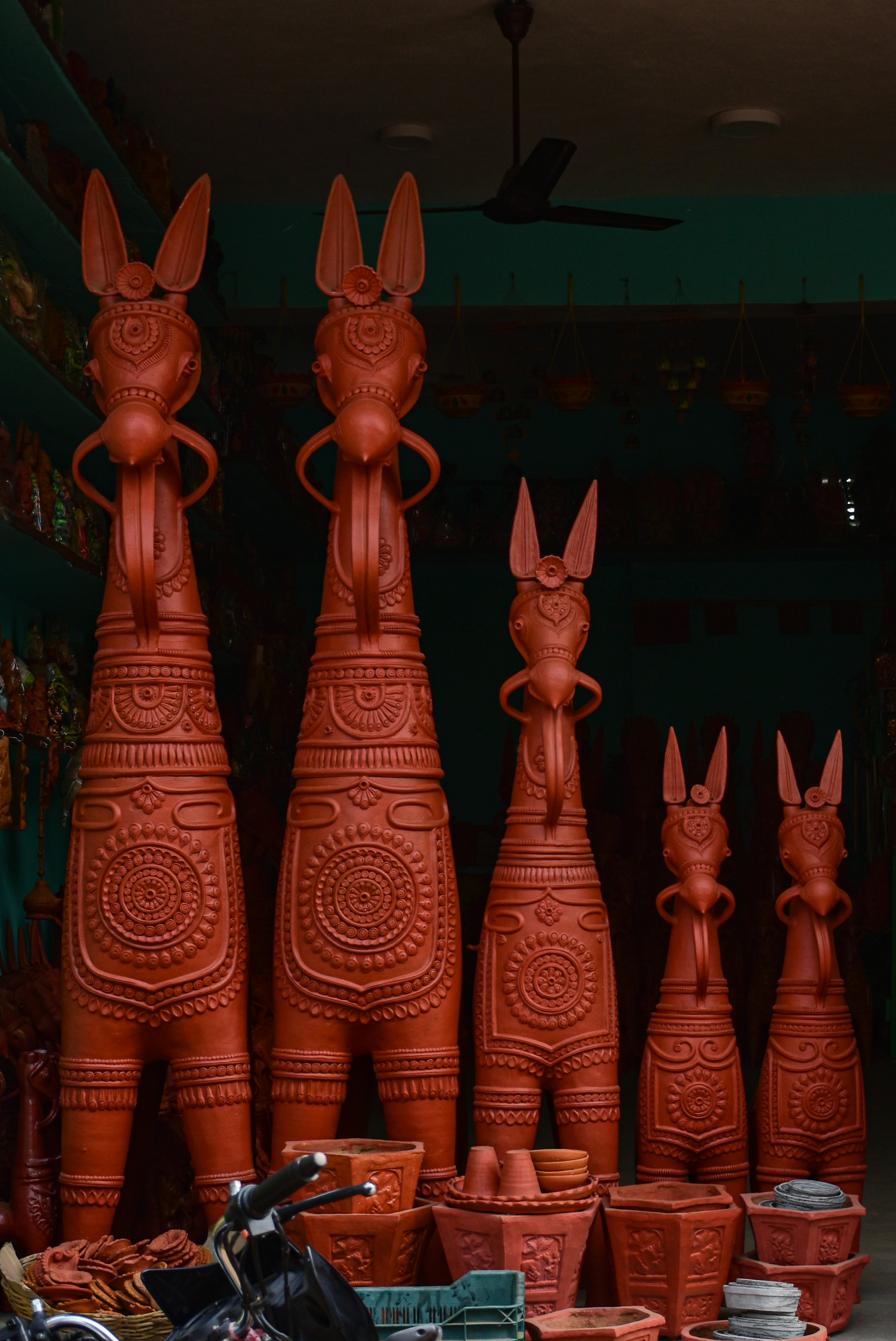 Crimson Sentinels: Tall Terracotta Figures in a Shaded Market Shrine