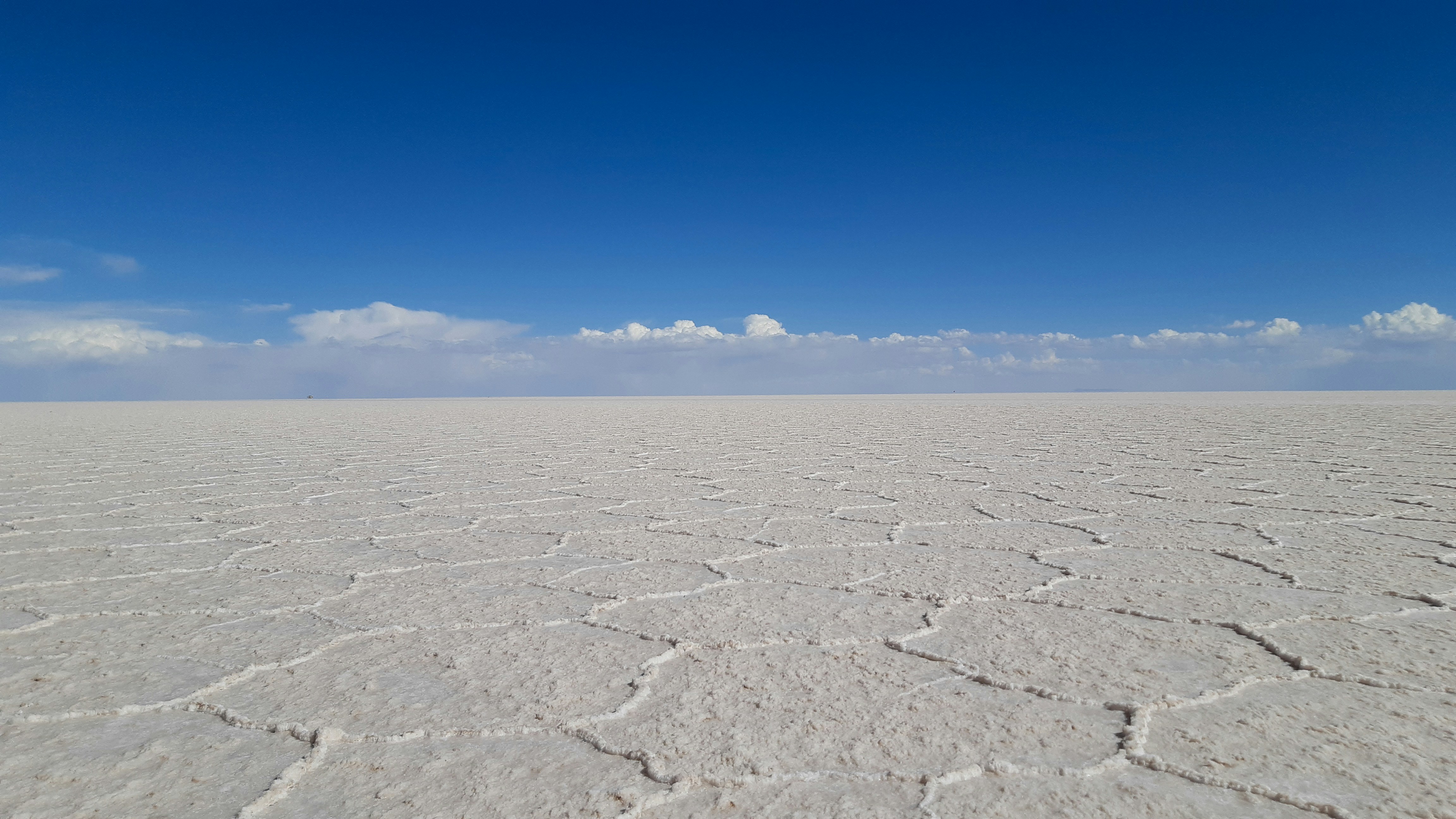 Vast white salt flats stretching to the horizon beneath a clear blue sky.