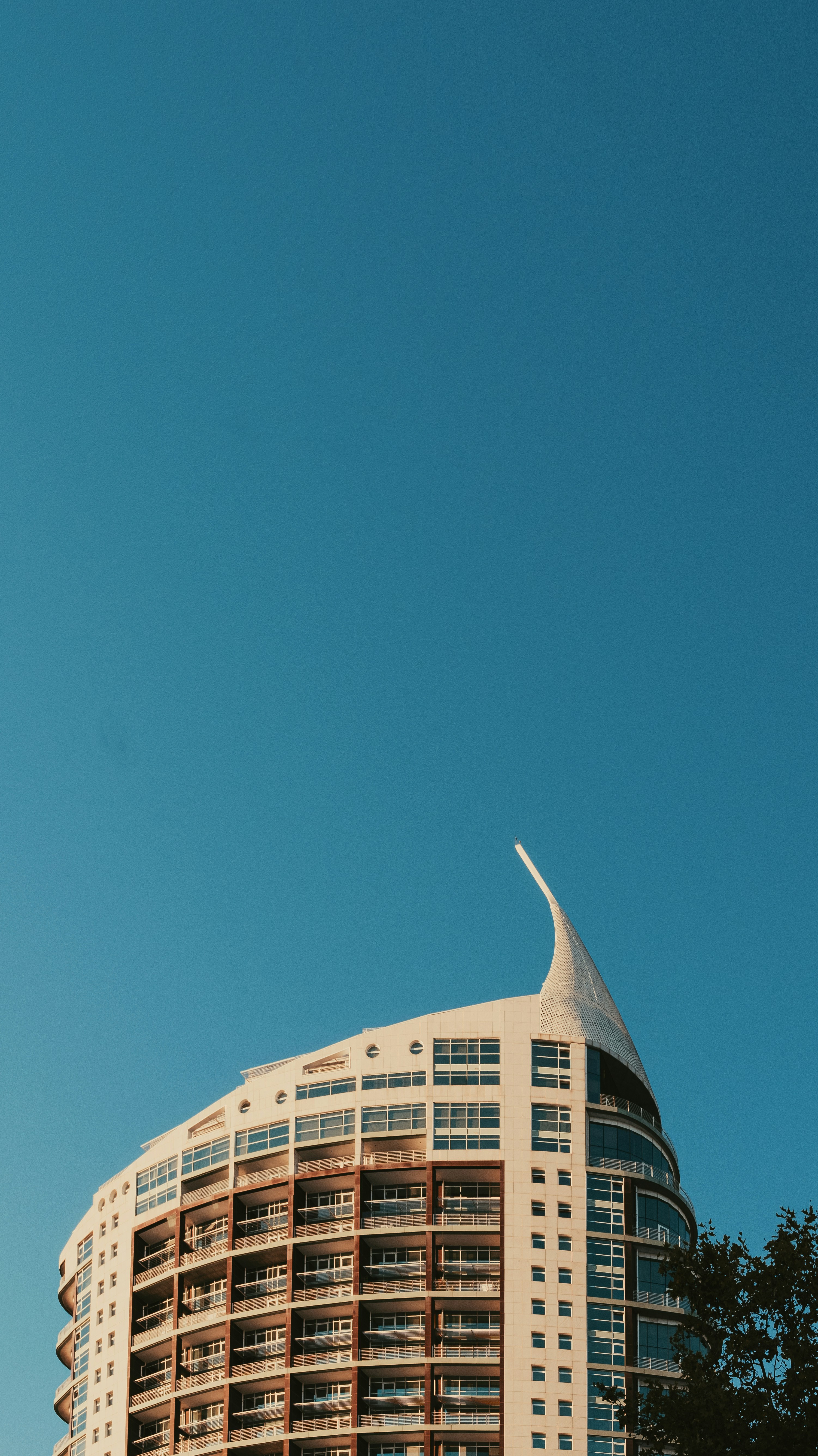 Modern building with a distinctive curved design and a pointed rooftop against a clear blue sky.