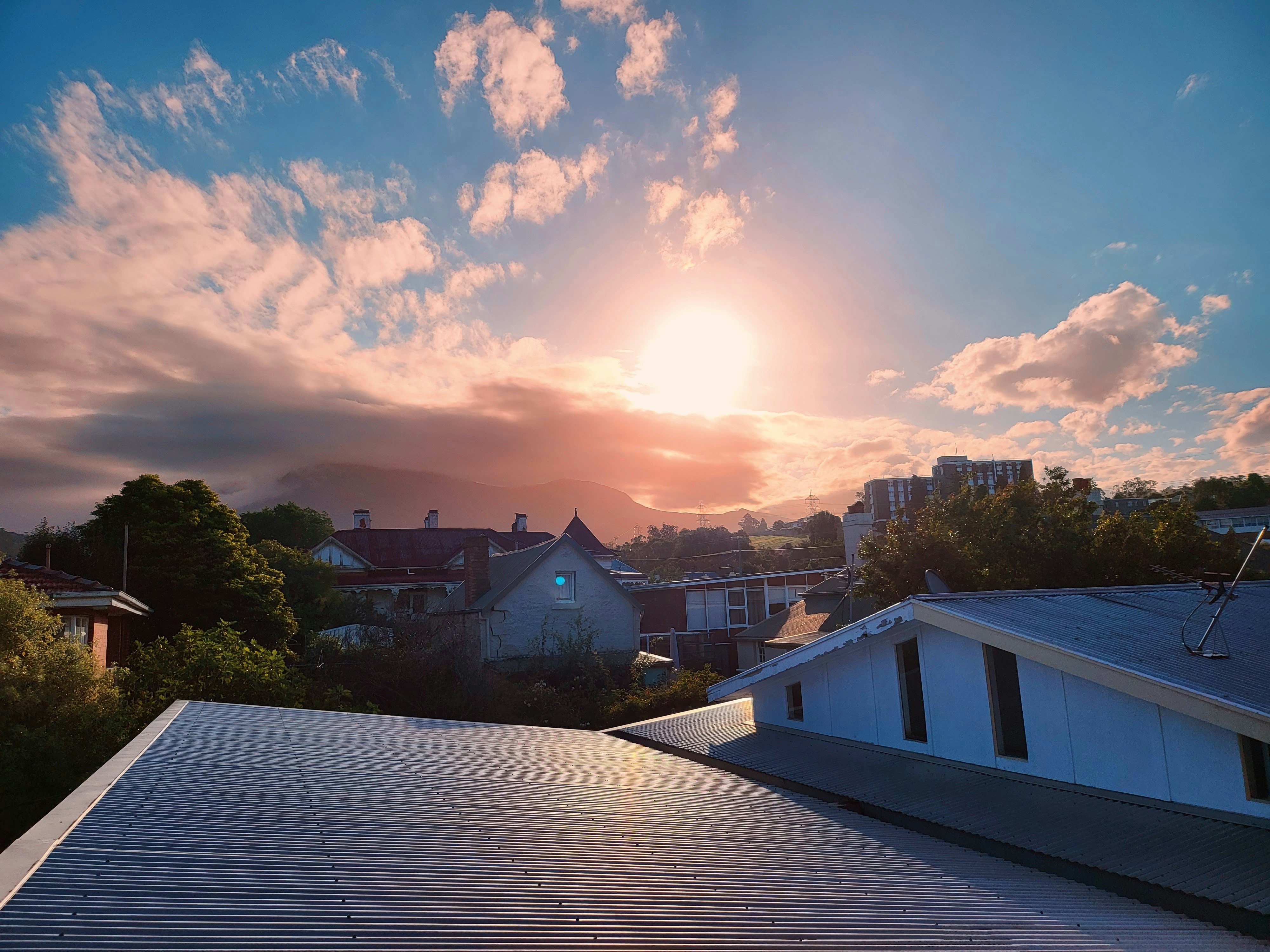 Golden sunlight spills over rooftops, illuminating clouds and casting a warm glow on the scene. The composition captures the tranquility of a new day.