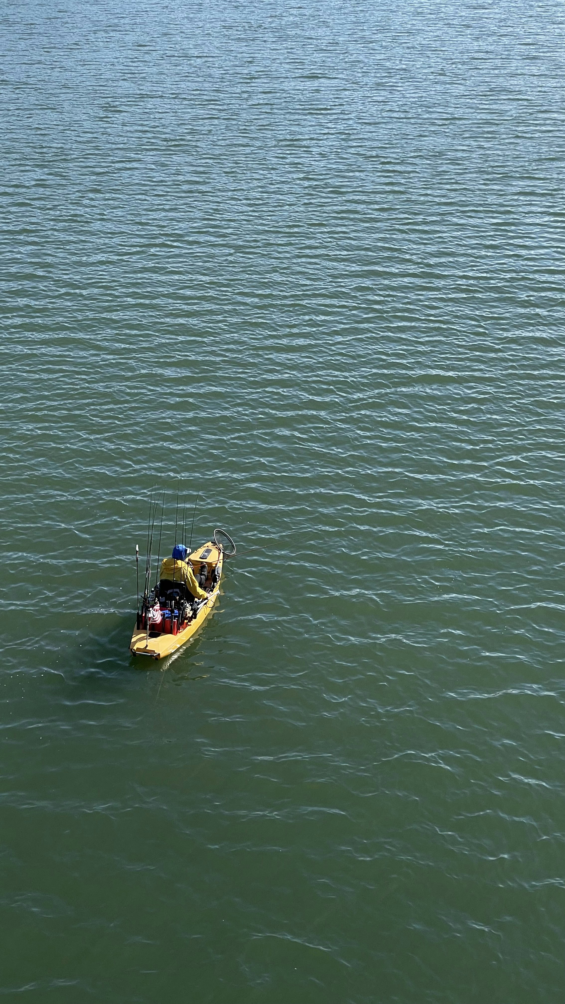 A lone kayaker equipped with fishing gear navigates calm waters under a clear sky.