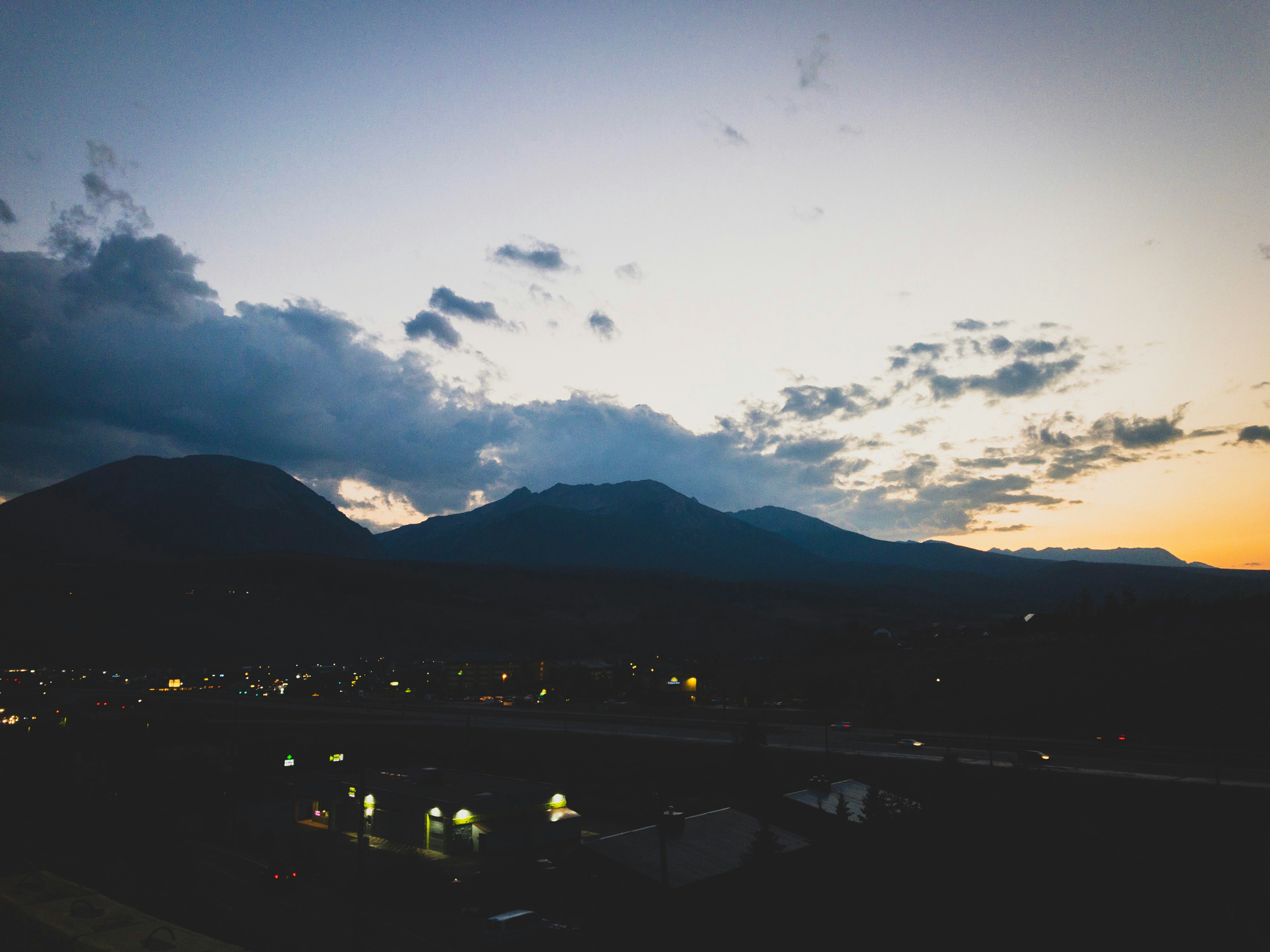 Distant mountains silhouetted against a twilight sky with city lights below.