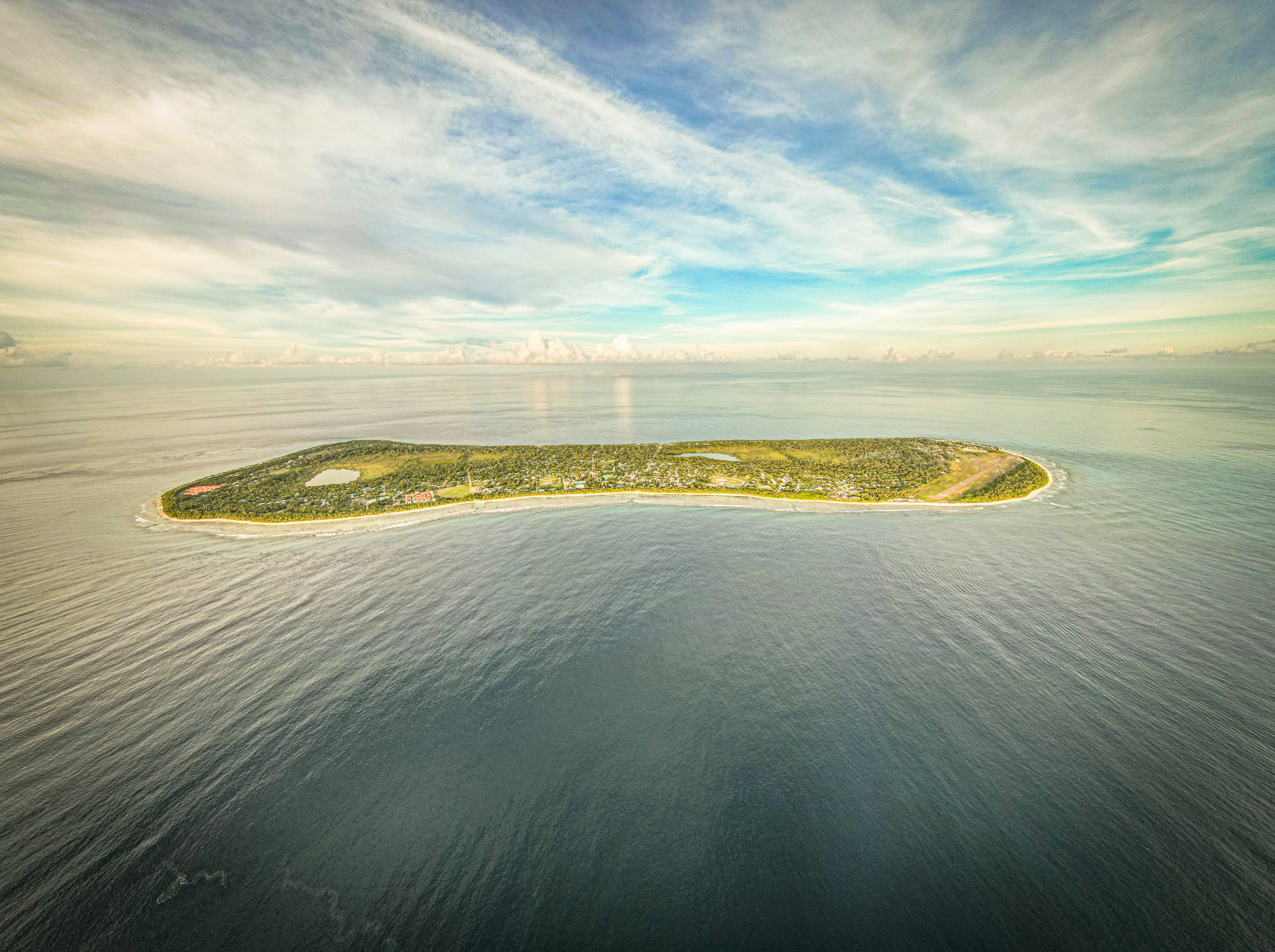Aerial view of a lush, elongated island surrounded by tranquil waters, showcasing vibrant greenery and a sandy shoreline.