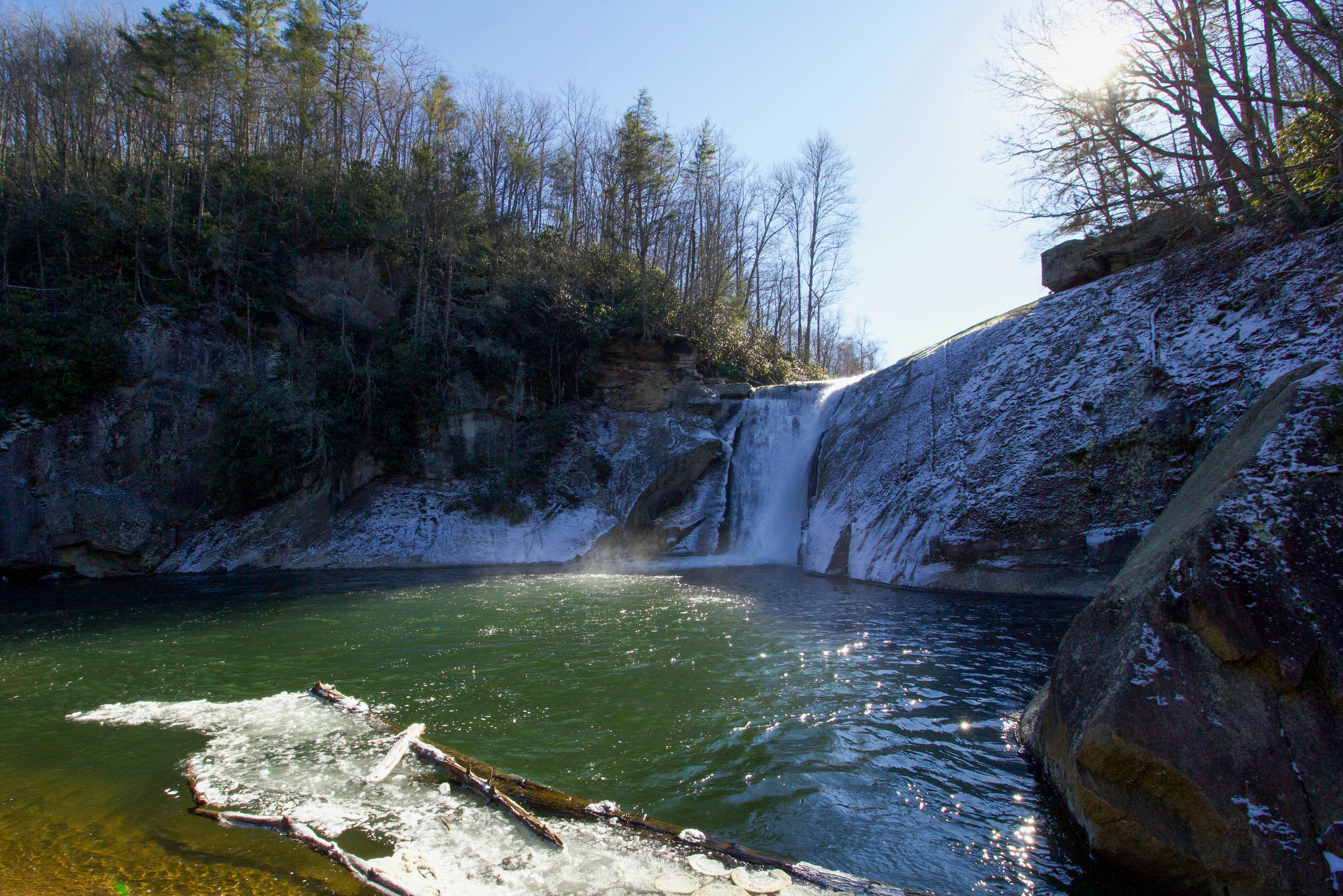A serene waterfall cascading over icy rocks, surrounded by a tranquil forest landscape. The scene captures the essence of winter's quiet beauty.