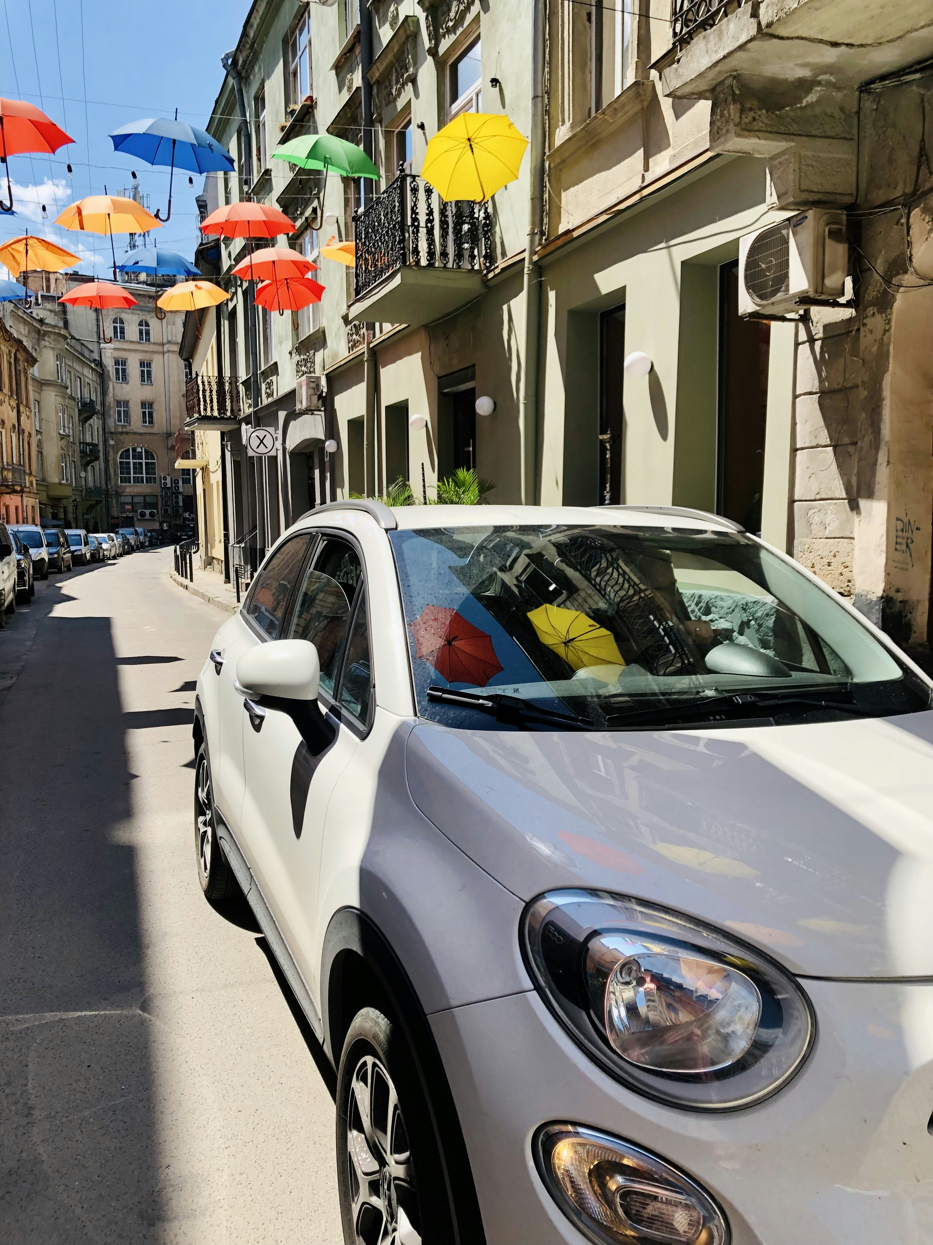 Colorful Umbrellas in a Sunlit Street: White SUV as the Quiet Anchor
