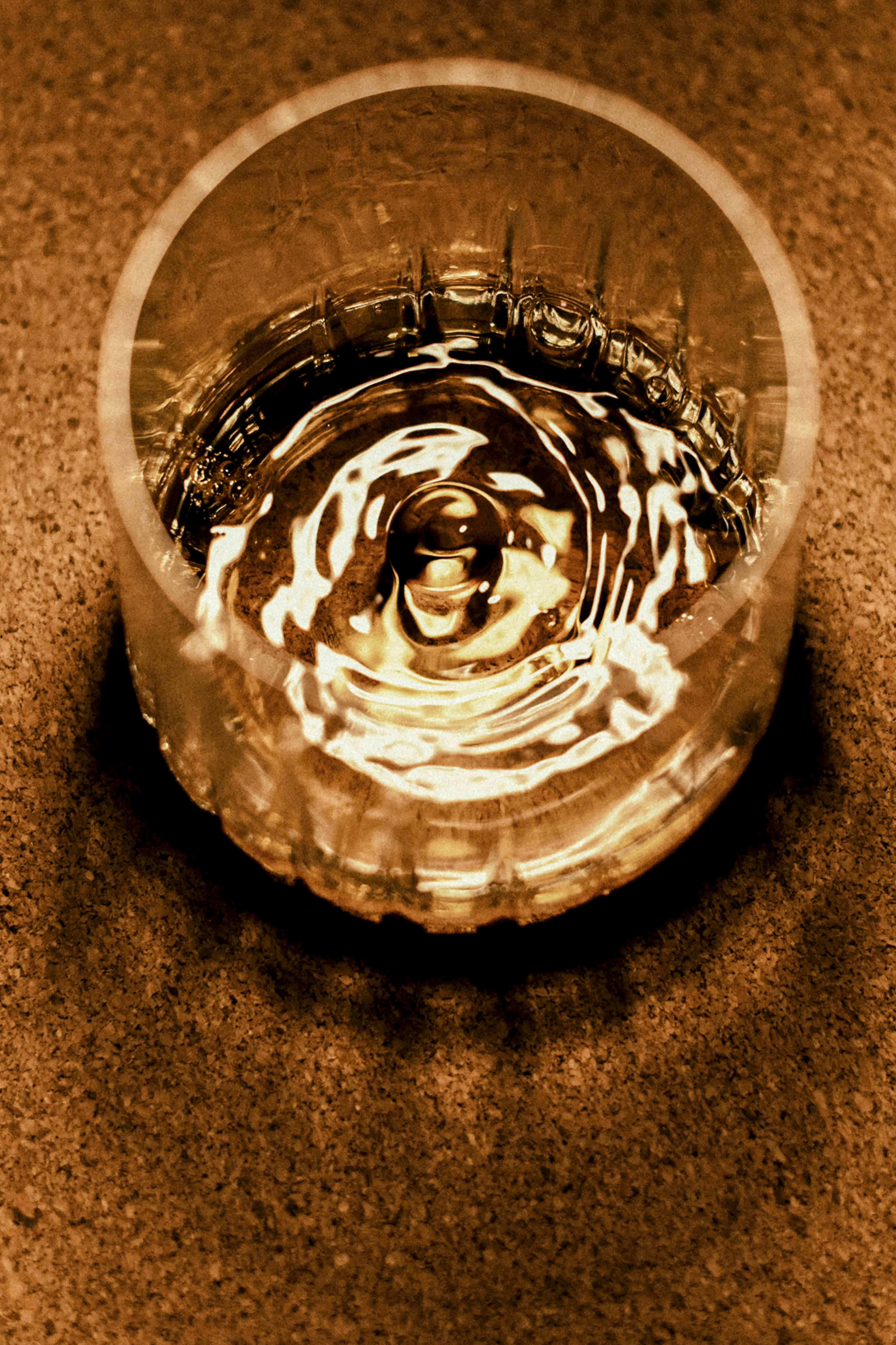 Amber Orbit: Close-up of a glass catching a sunlit ripple on a terrazzo surface