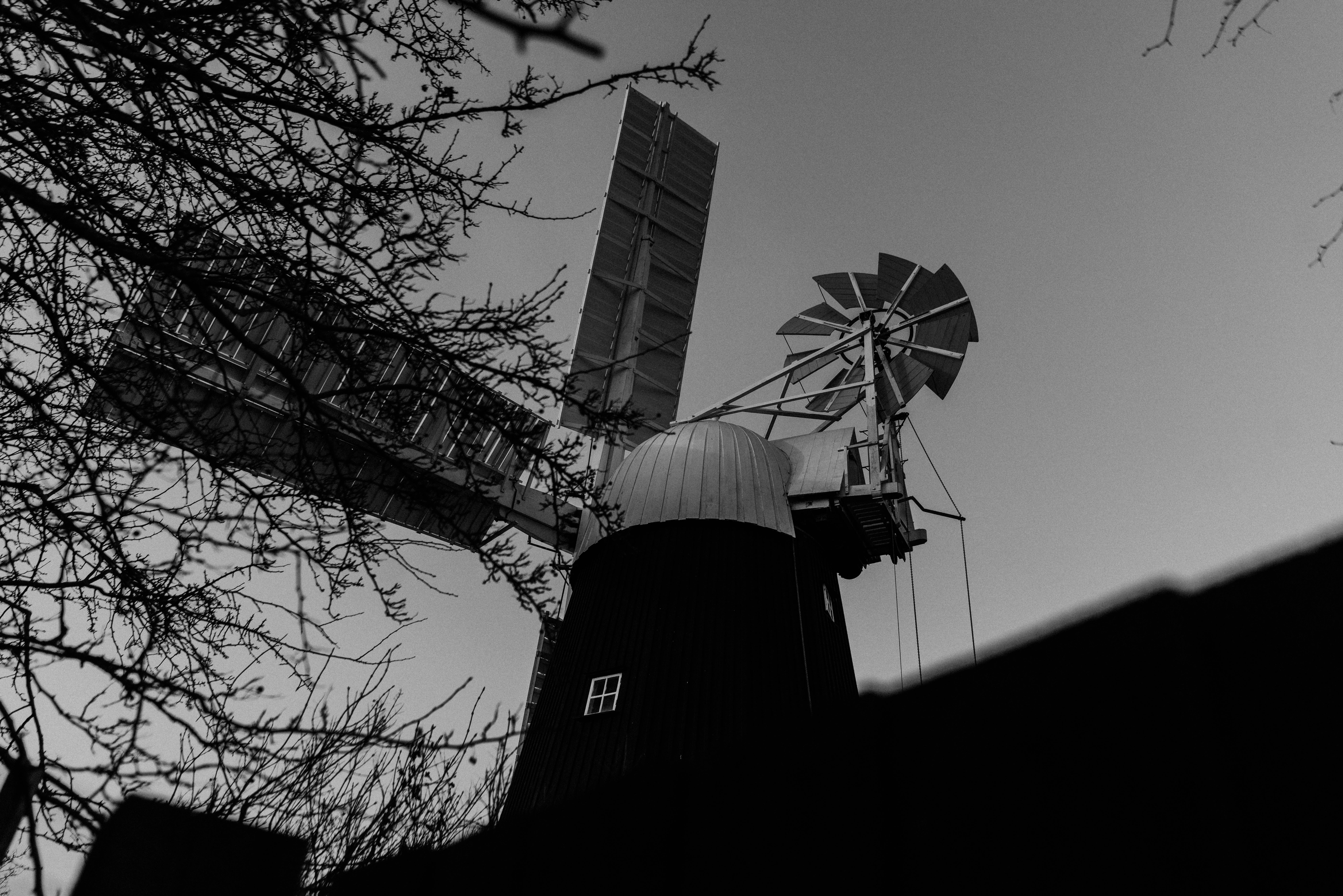 Historic windmill silhouetted against a twilight sky, framed by bare branches. The structure stands as a testament to traditional craftsmanship.